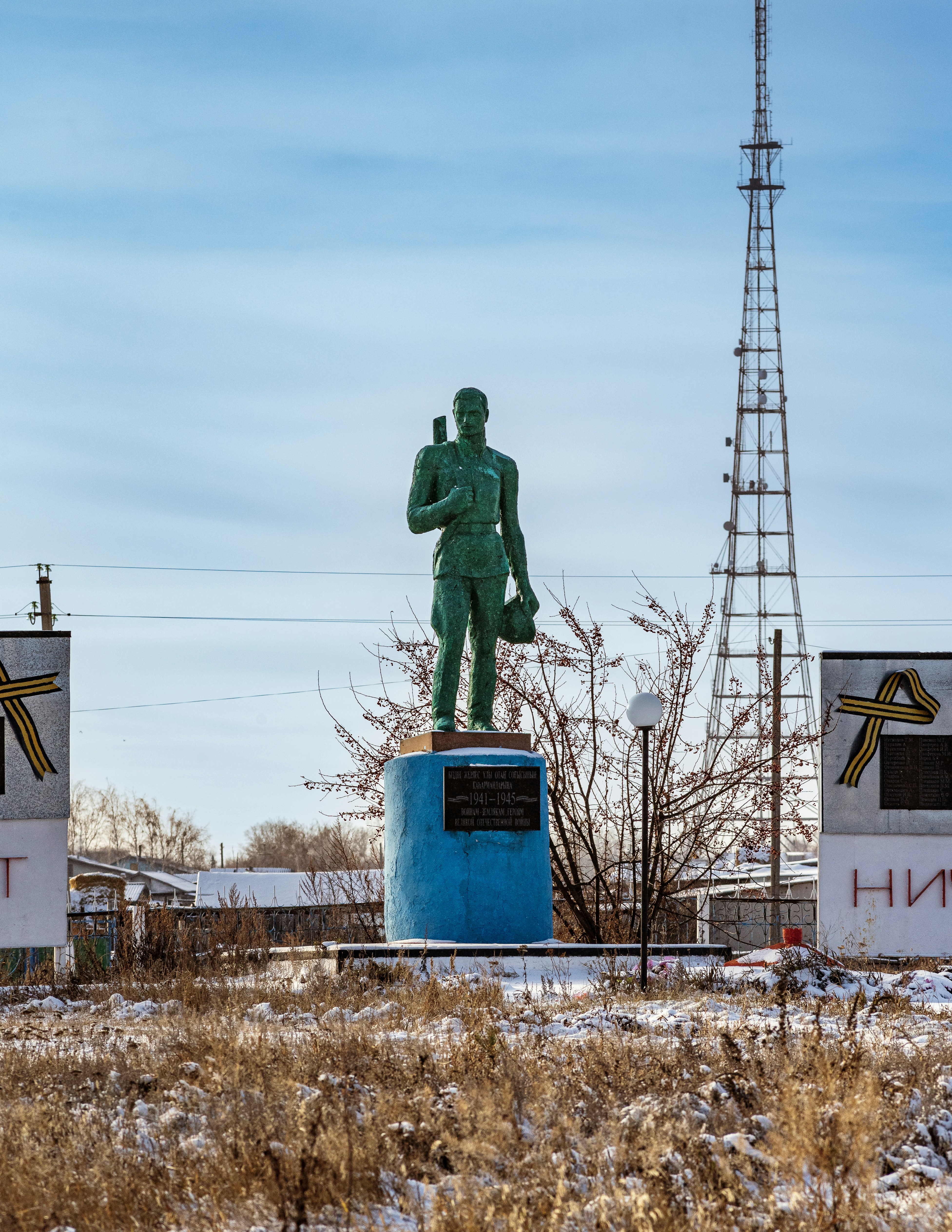 Statue on a Blue Pedestal Under a Clear Sky, with Radio Tower in a Secluded Town