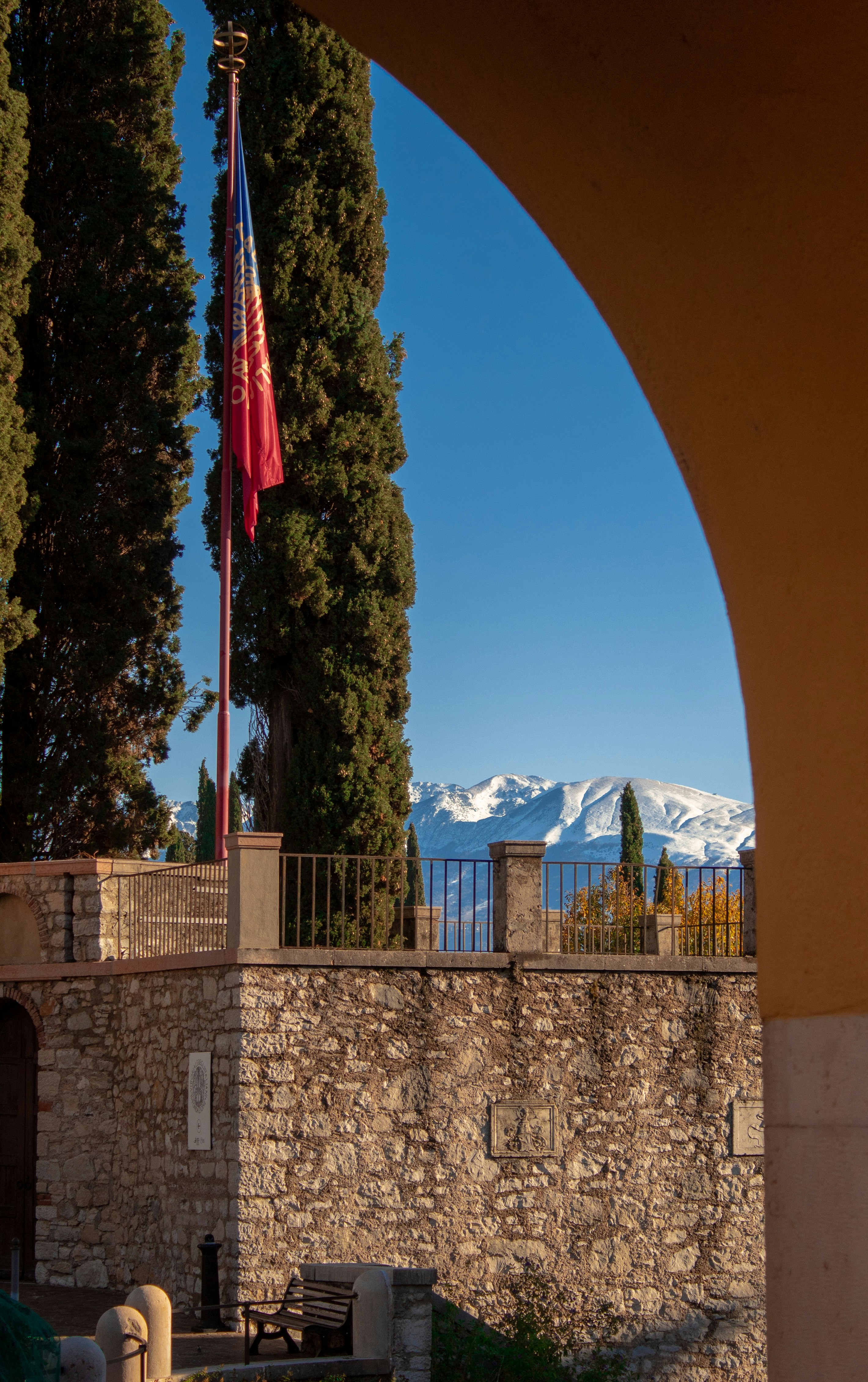 Mountain view from Vittoriale degli italiani with flag, trees and arch in the front