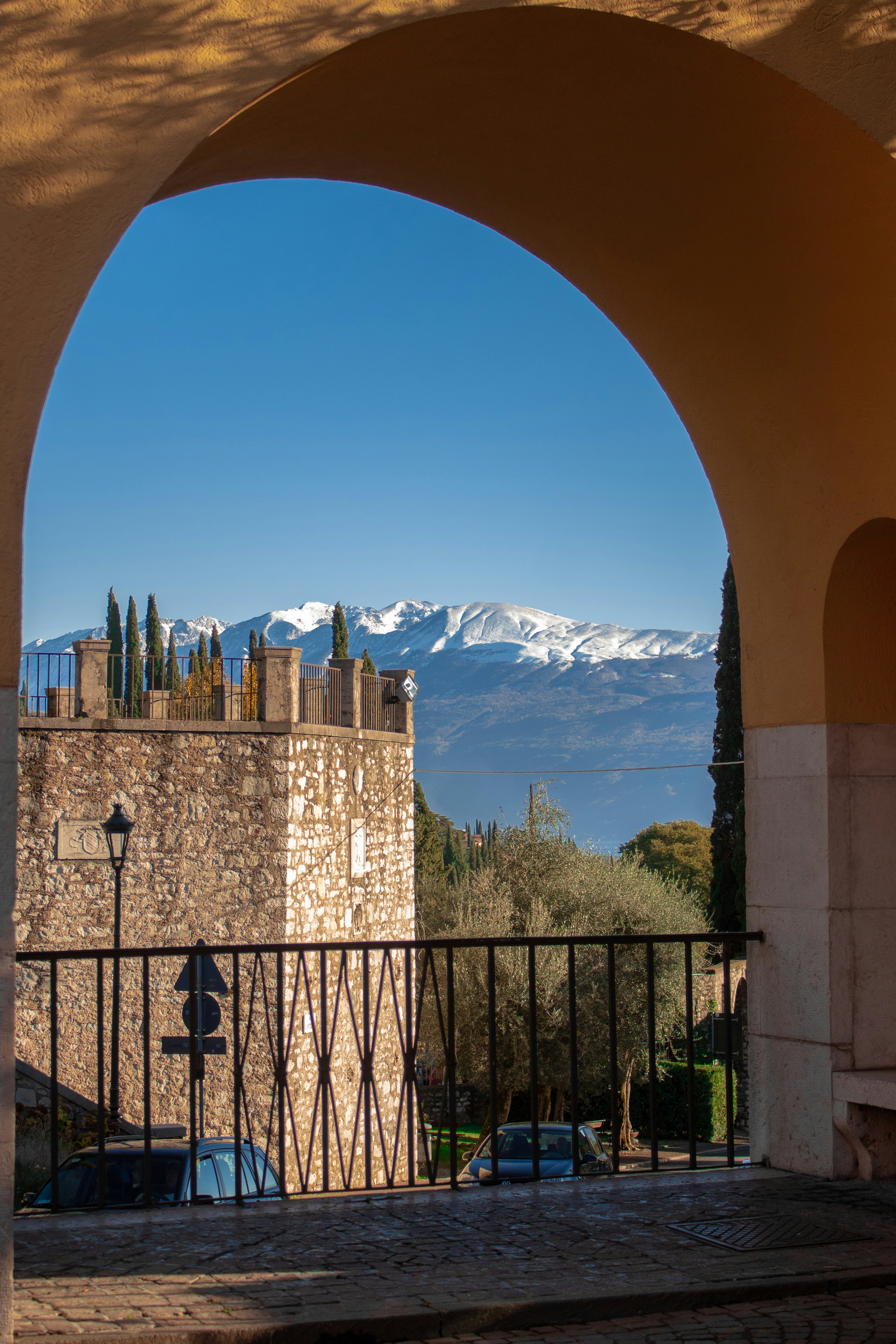 Archway Vista: Snow-Capped Peaks Beyond a Sunlit Stone Courtyard