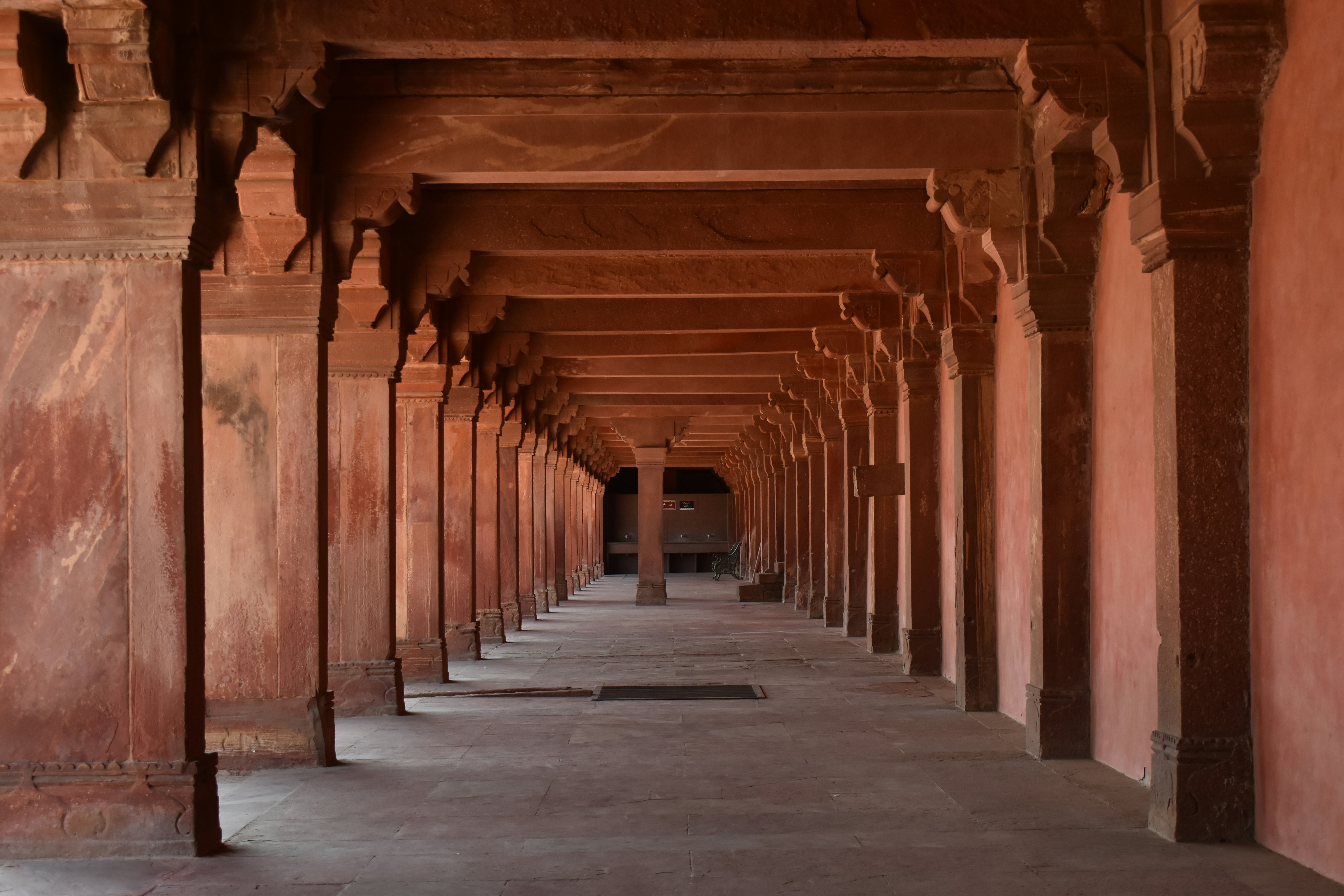 Long corridor with repeating red sandstone arches in symmetrical perspective.