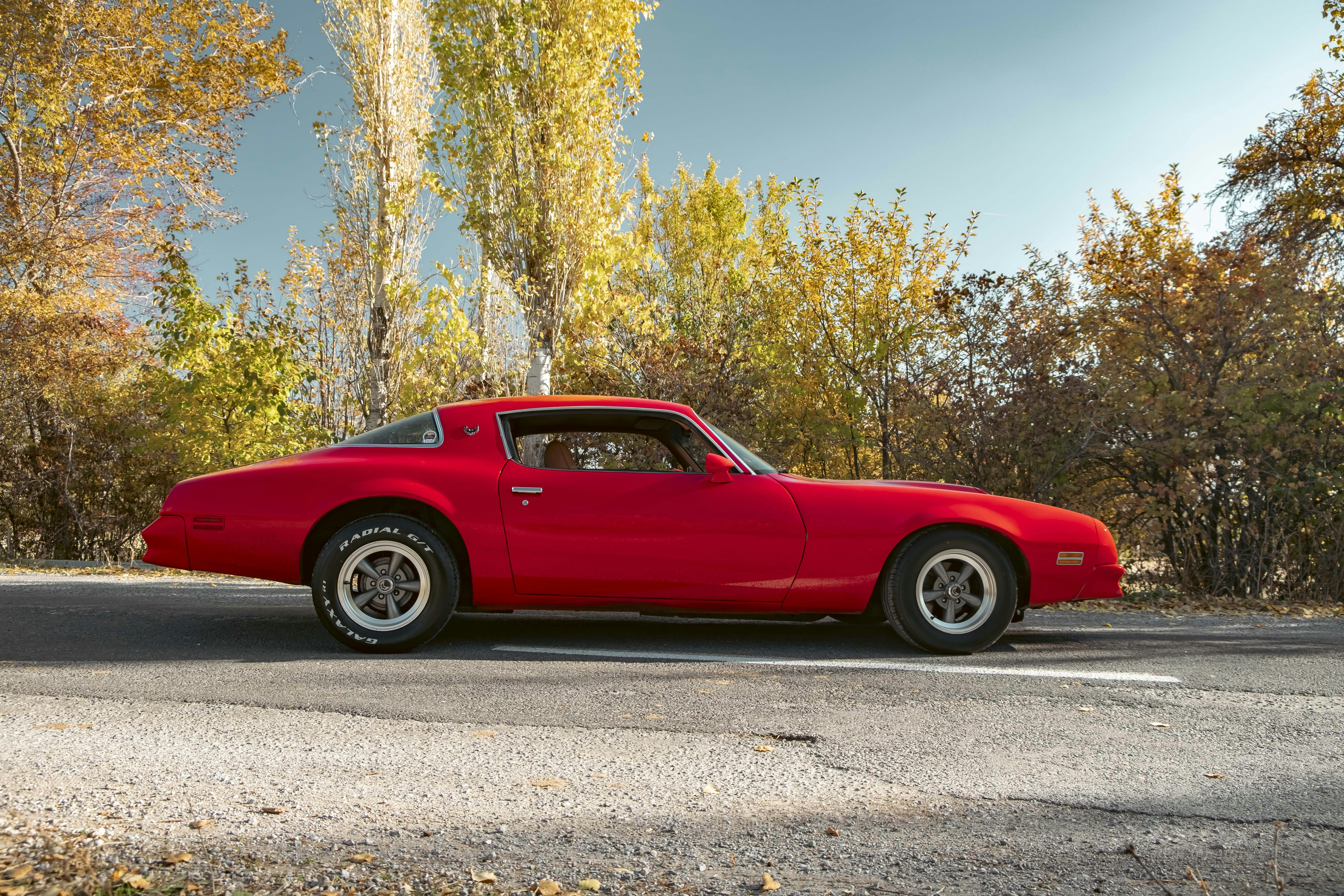 Vintage red sports car parked on a road surrounded by vibrant autumn foliage.