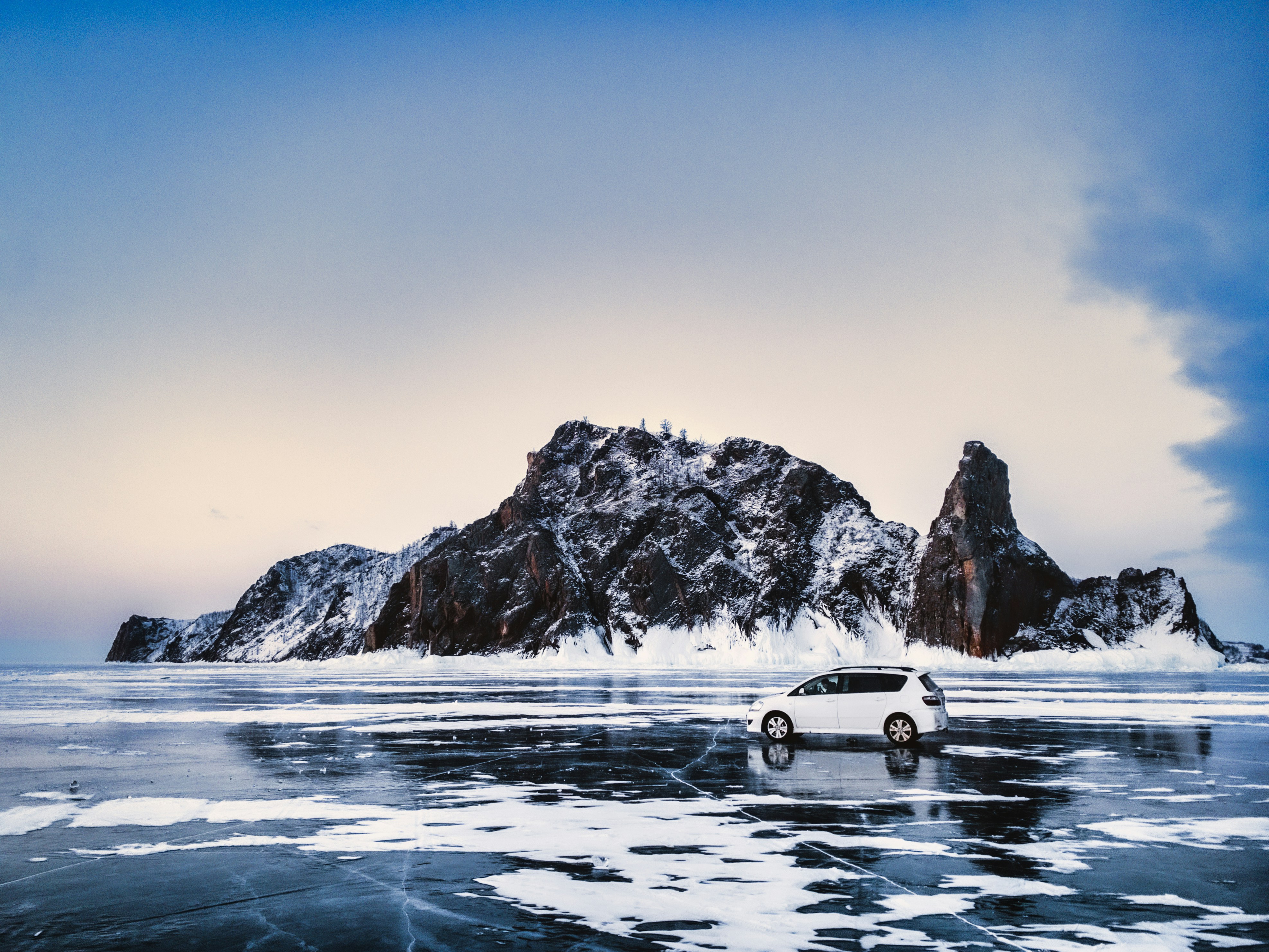 Cracked Ice Crossing: White SUV on a Frozen Lake Before a Snow-Dusted Island