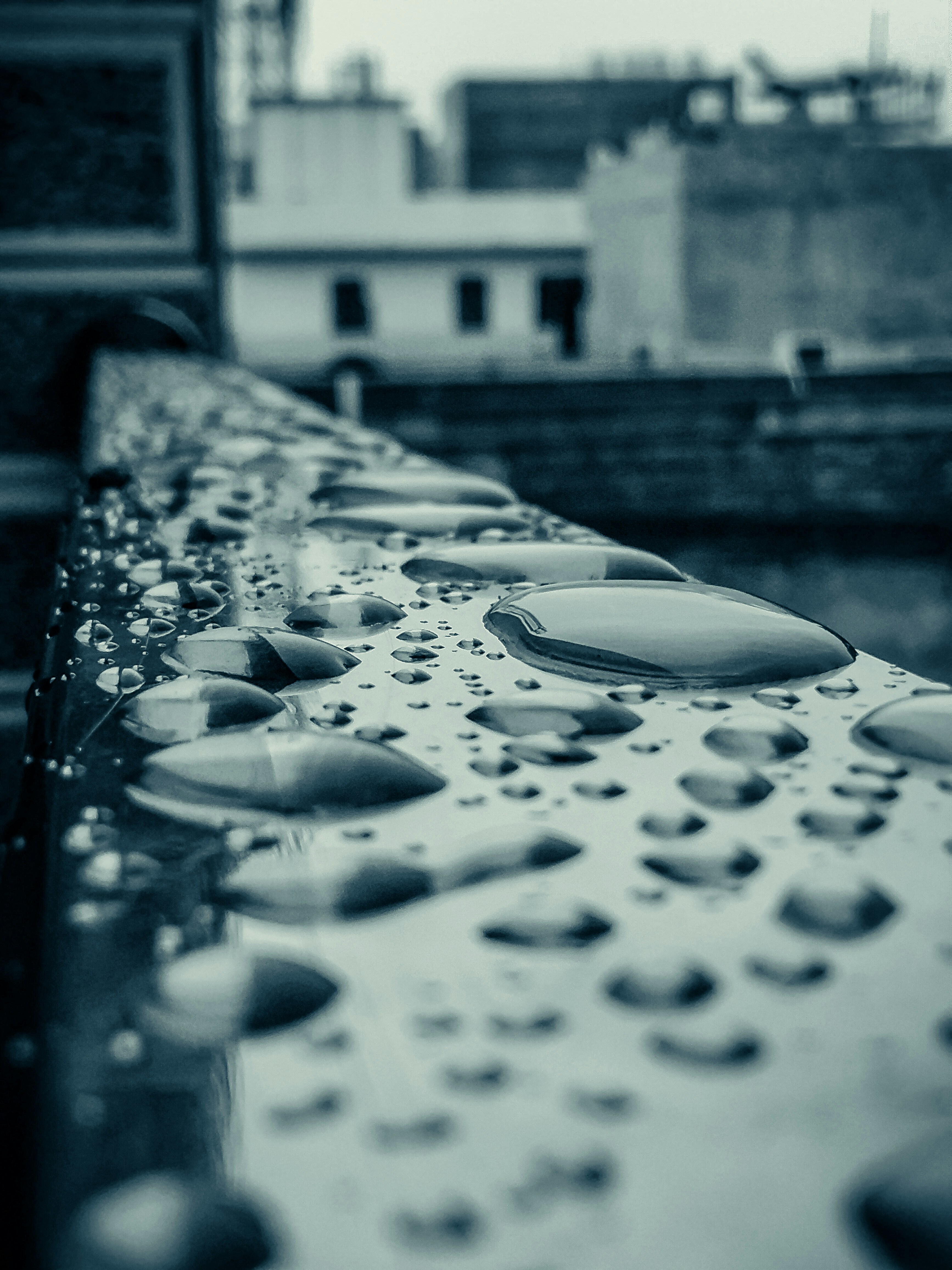 Rain-Glossed Rail: Drops in Focus Against a Cityscape Blur
