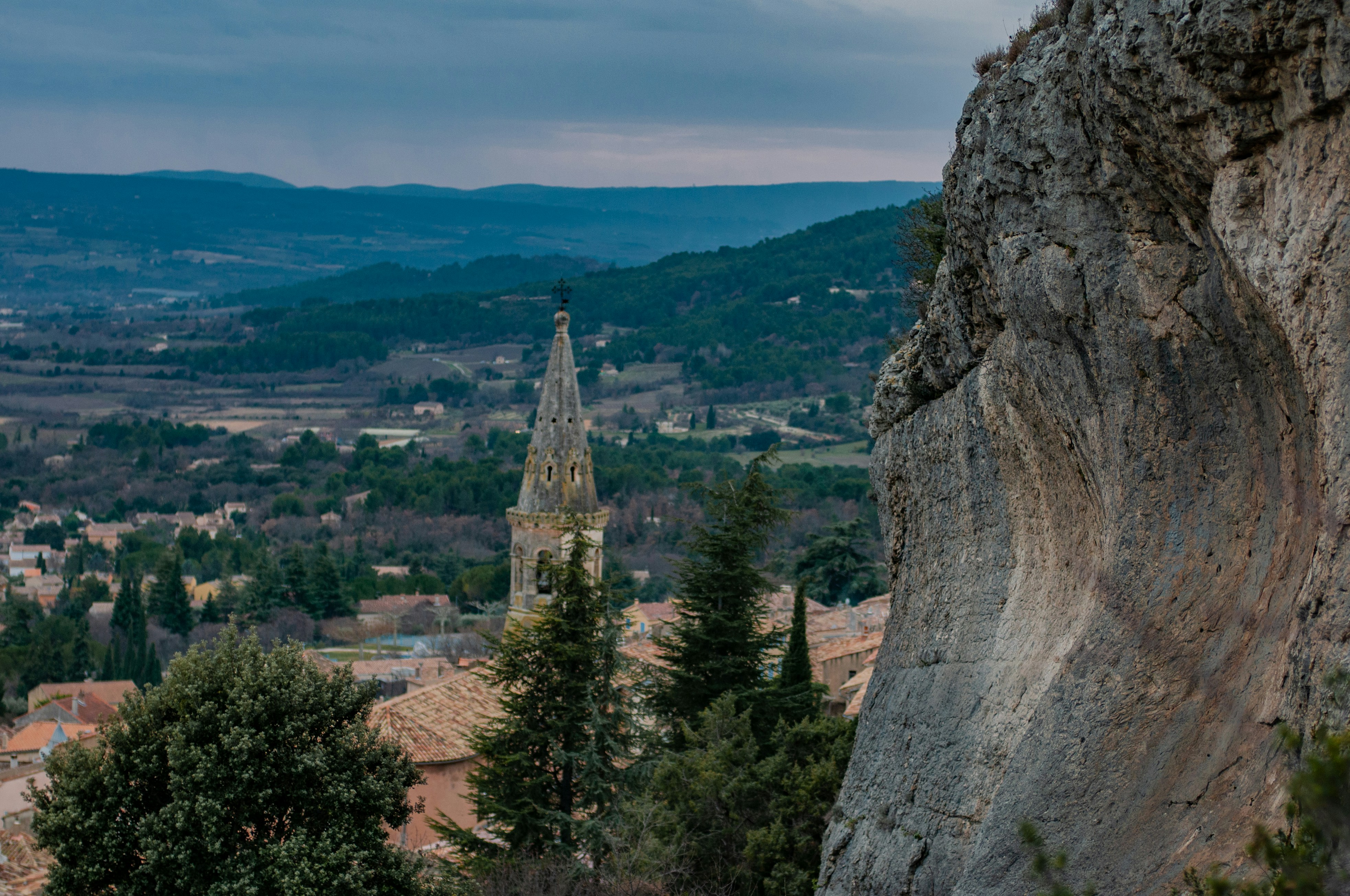 Historic church tower rising above a tranquil landscape, framed by rugged cliffs and lush greenery.