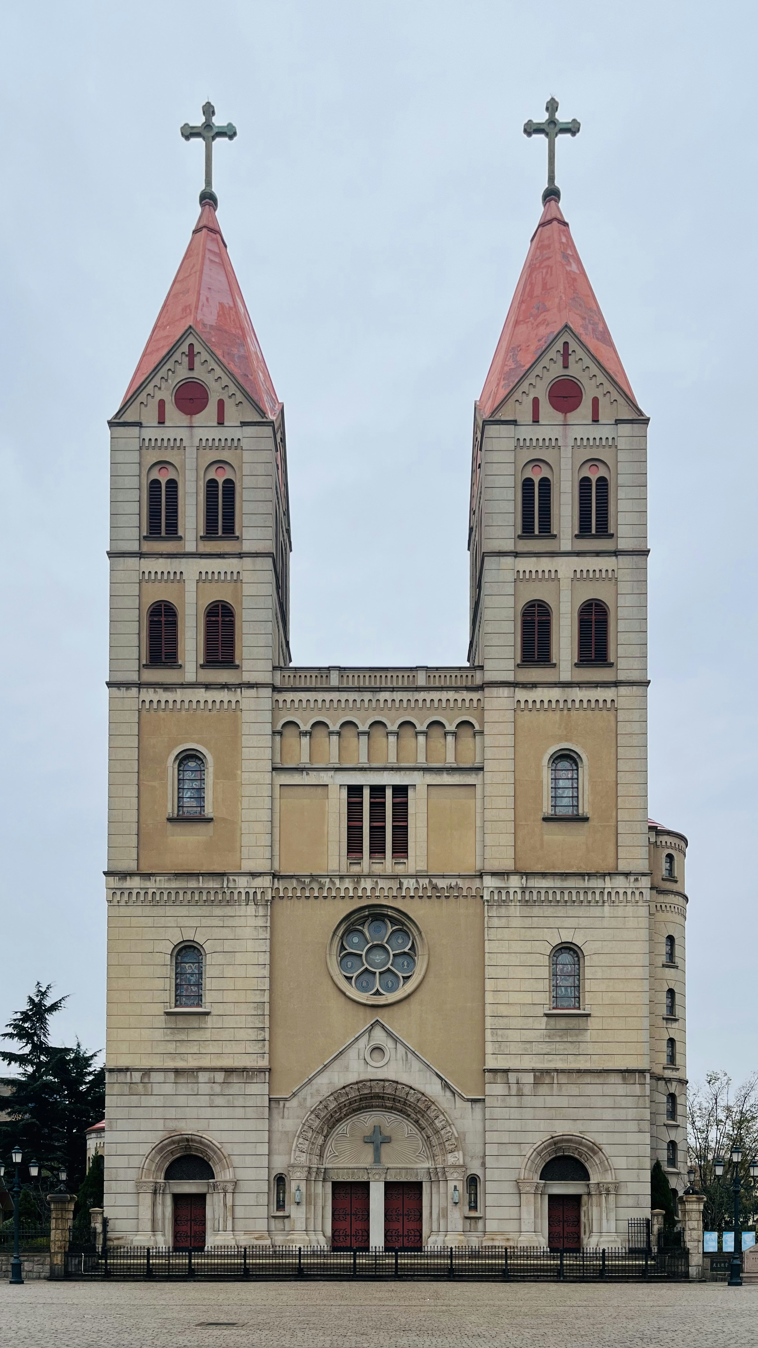 Historic church with twin spires and a large rose window, showcasing a blend of architectural styles. The structure stands prominently against a cloudy sky.
