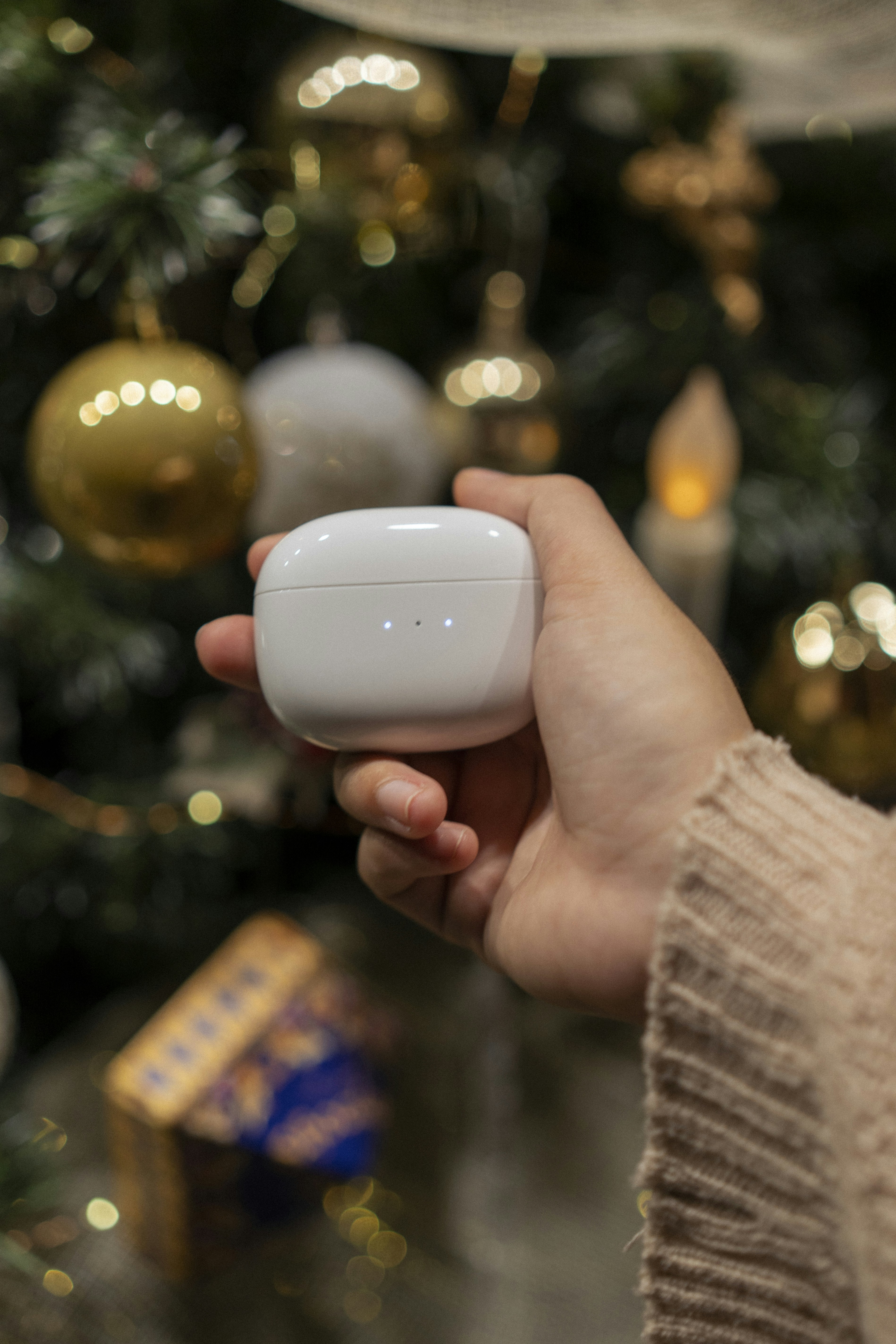 White wireless earbuds case held against a festive bokeh background