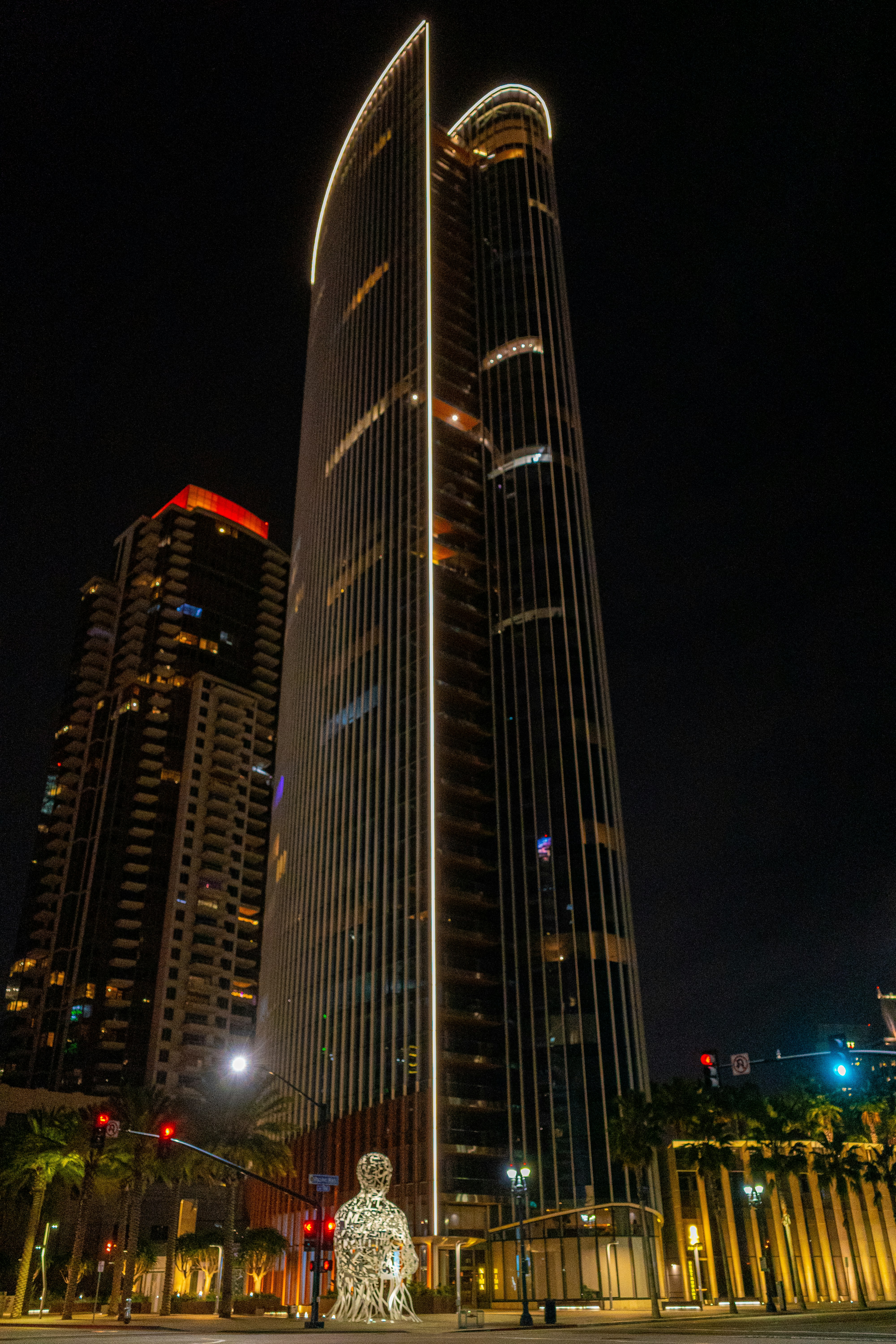 A towering skyscraper illuminated with elegant LED accents stands against a night sky, complemented by a striking wireframe sculpture in the foreground. The scene captures the vibrant energy of urban life.