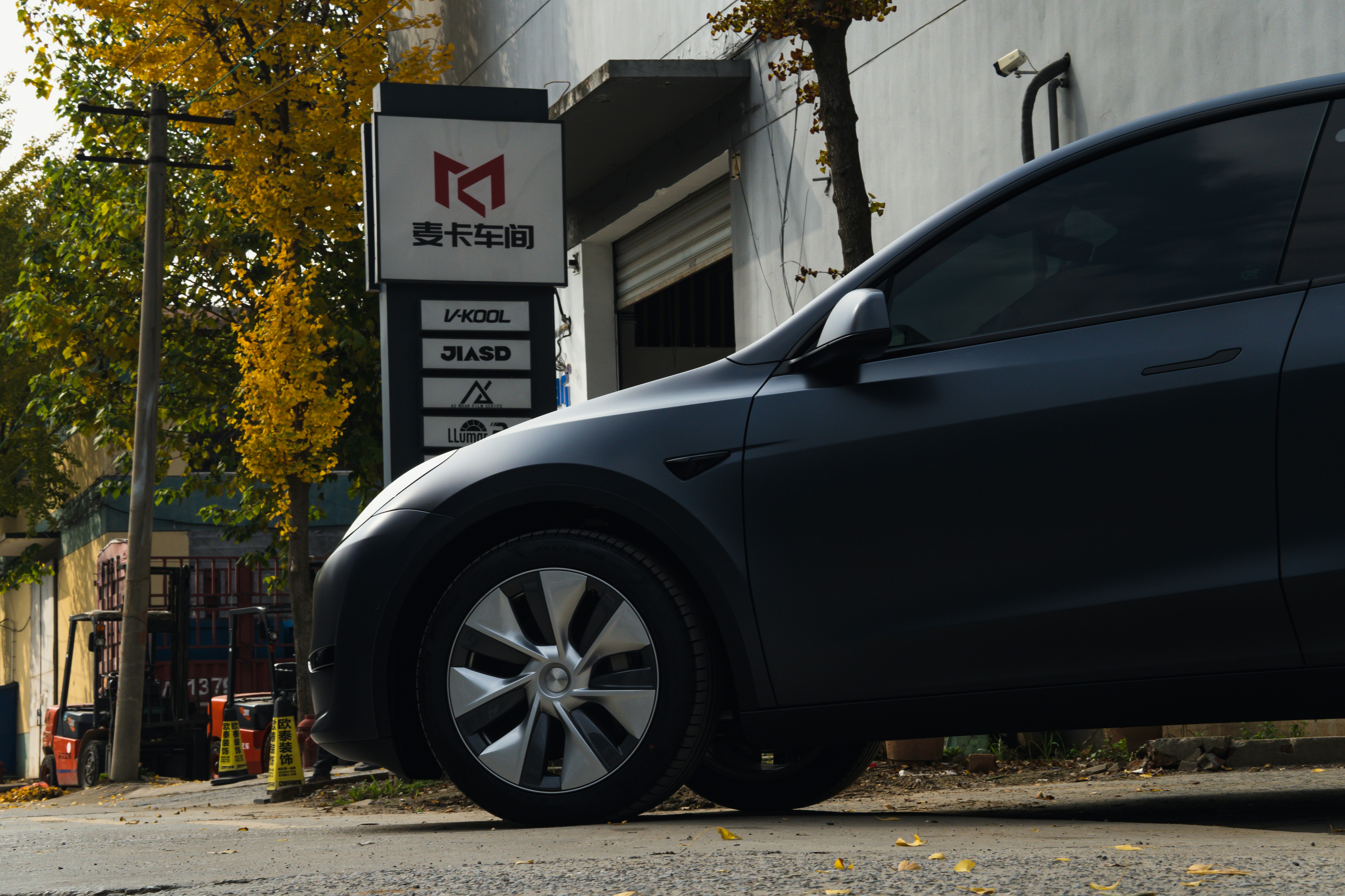 Low-Angle Street Moment: The Matte Gray Sedan's Wheel in an Autumn City Scene