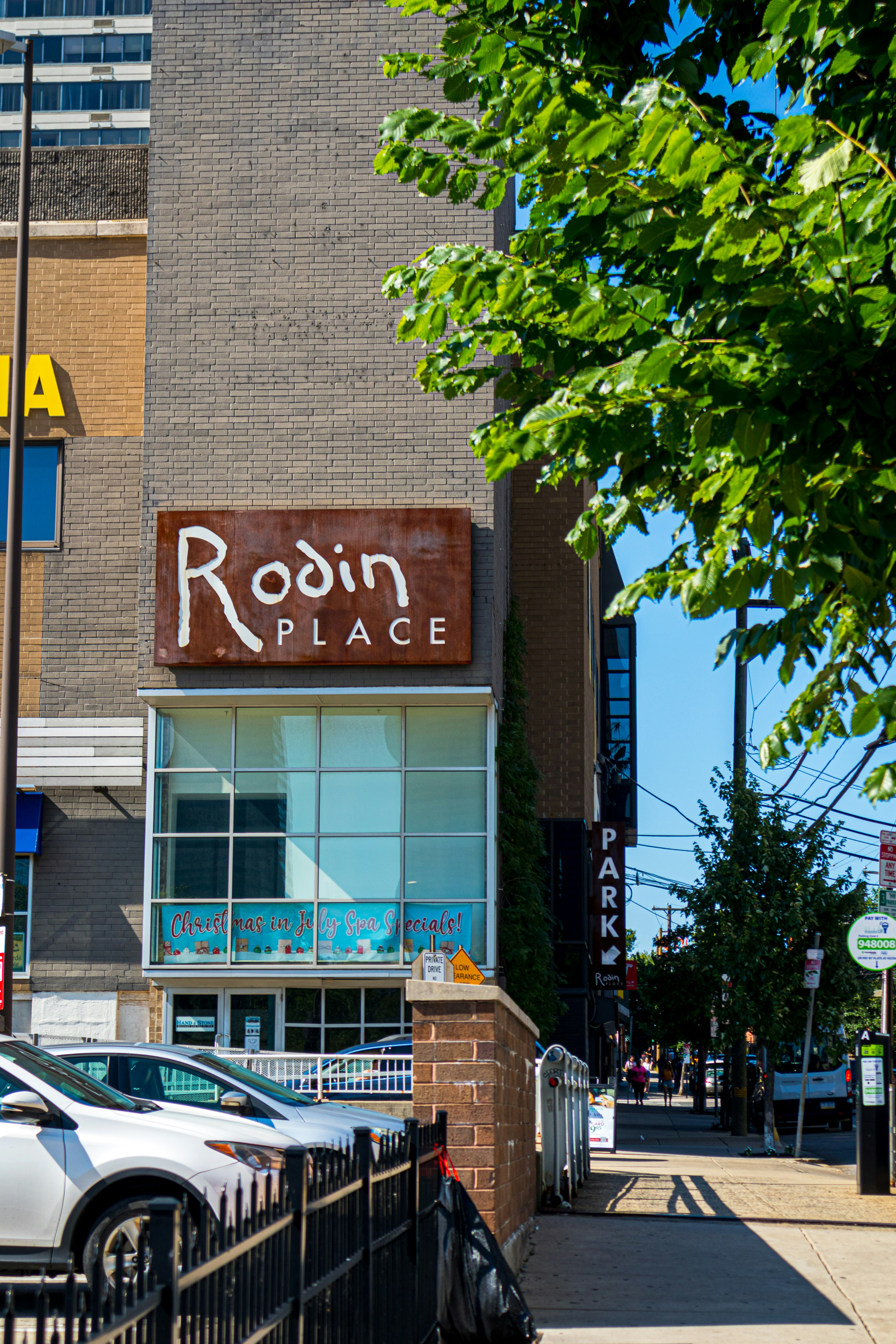 Rodin Place: Urban storefront with verdant shade and sunlit sidewalk