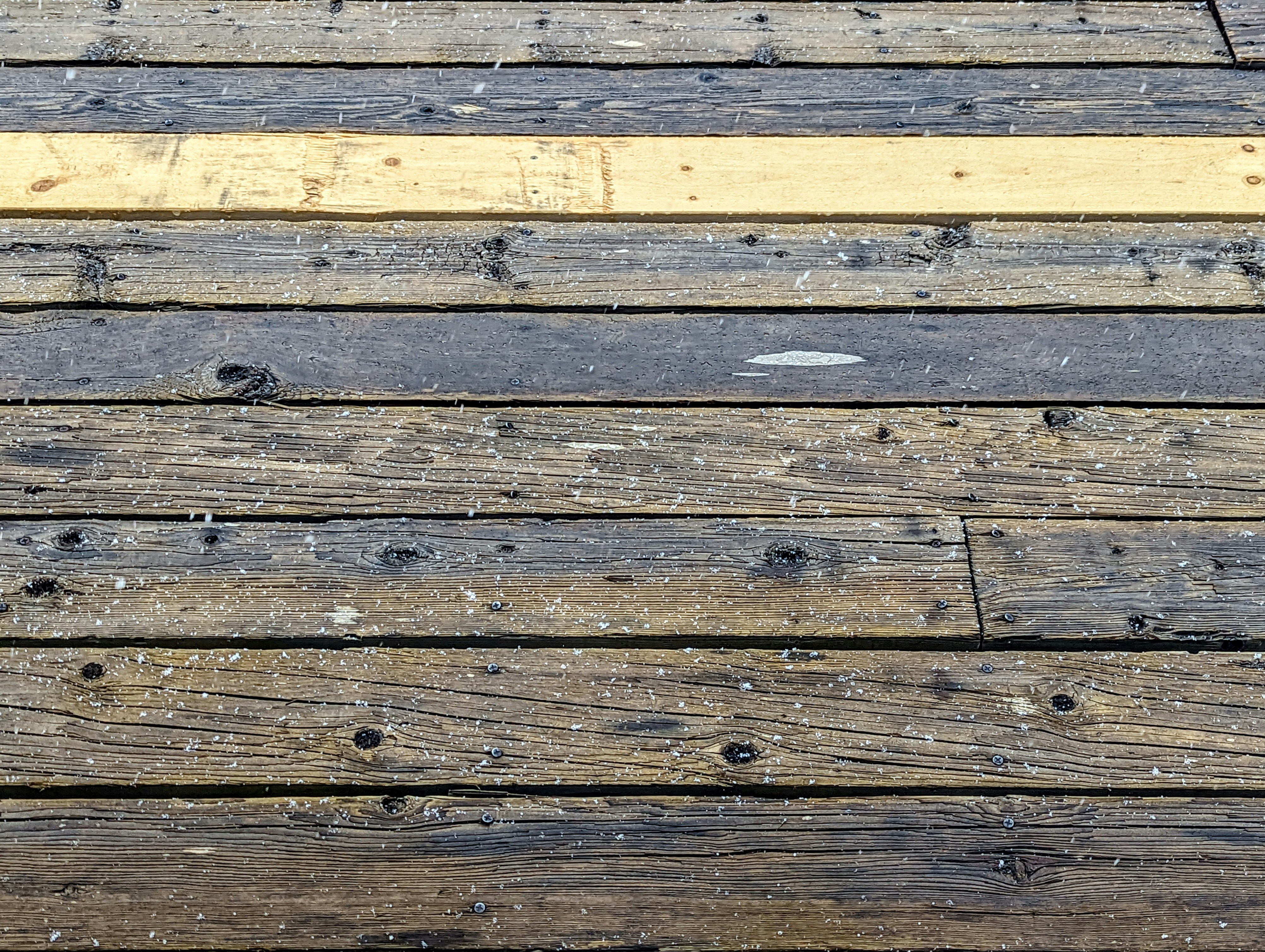 Close-up of weathered wooden planks showcasing a mix of natural hues and textures with a single yellow plank contrasting the earthy tones.
