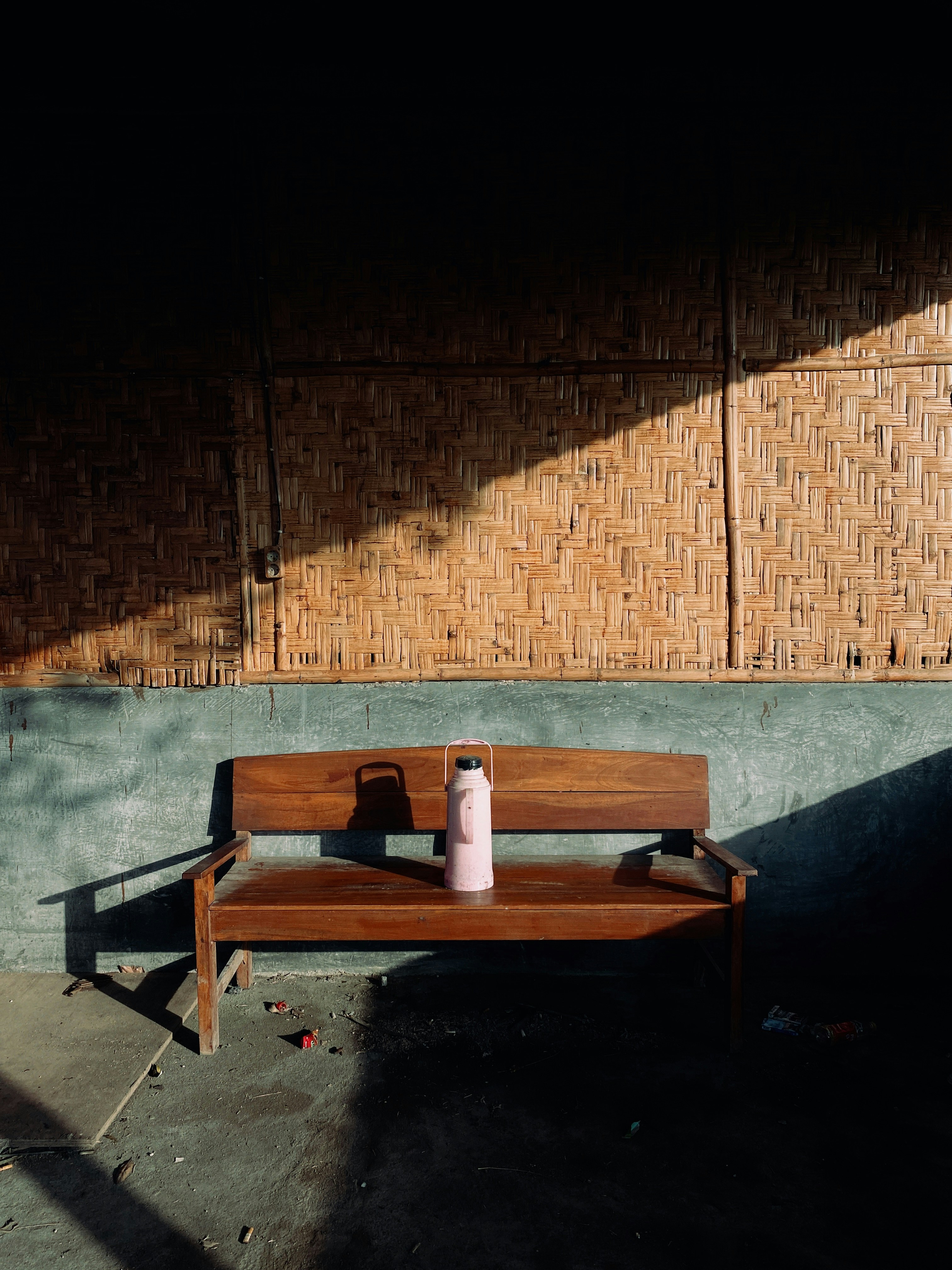 Pink Thermos on a Quiet Bench Under a Woven Wall's Diagonal Shadow
