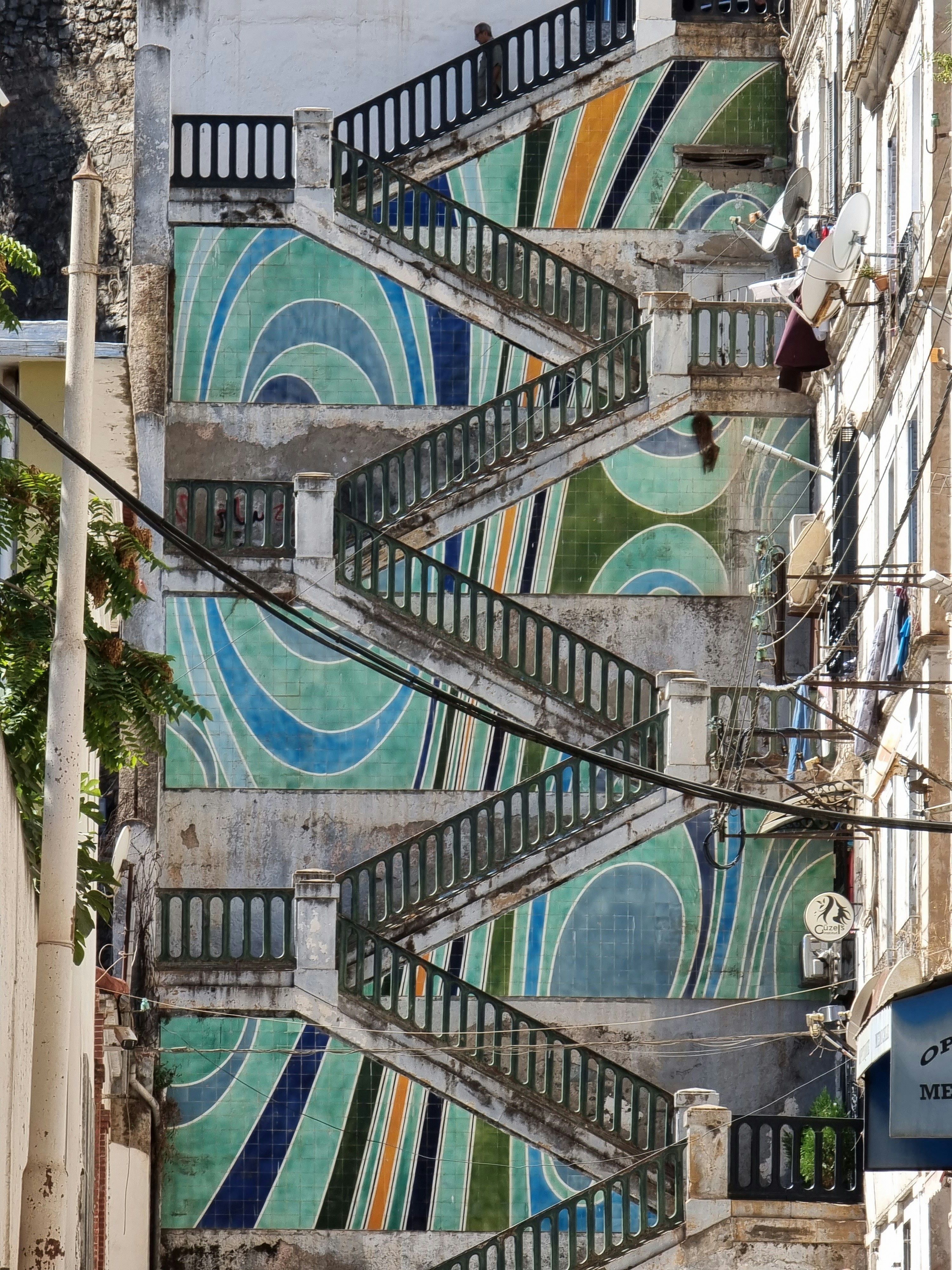 Colorful mural adorning a staircase, showcasing swirling patterns and geometric designs against a weathered backdrop.