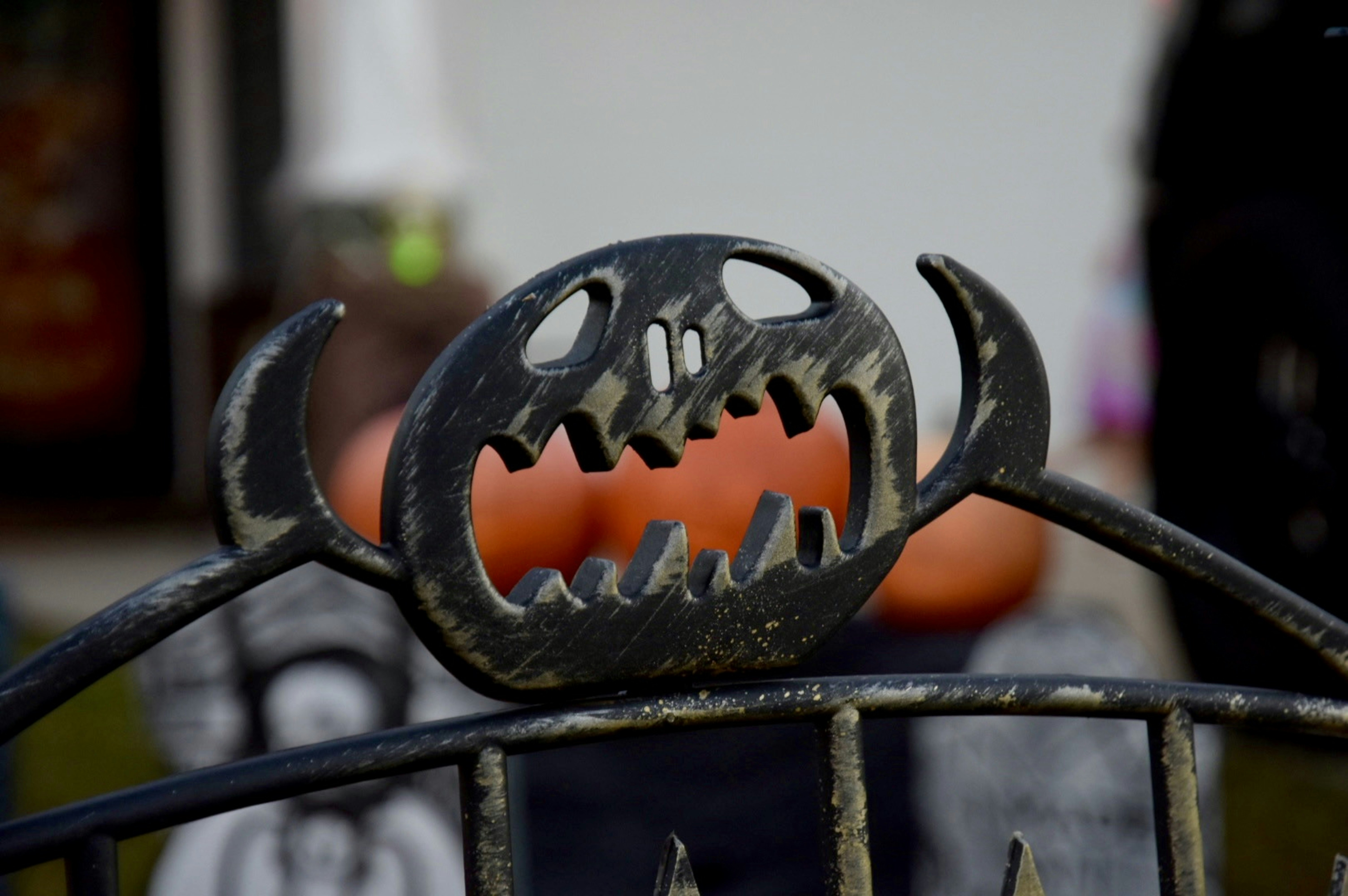 Grim Gate: A wrought-iron pumpkin-topped silhouette guards a blurred storefront