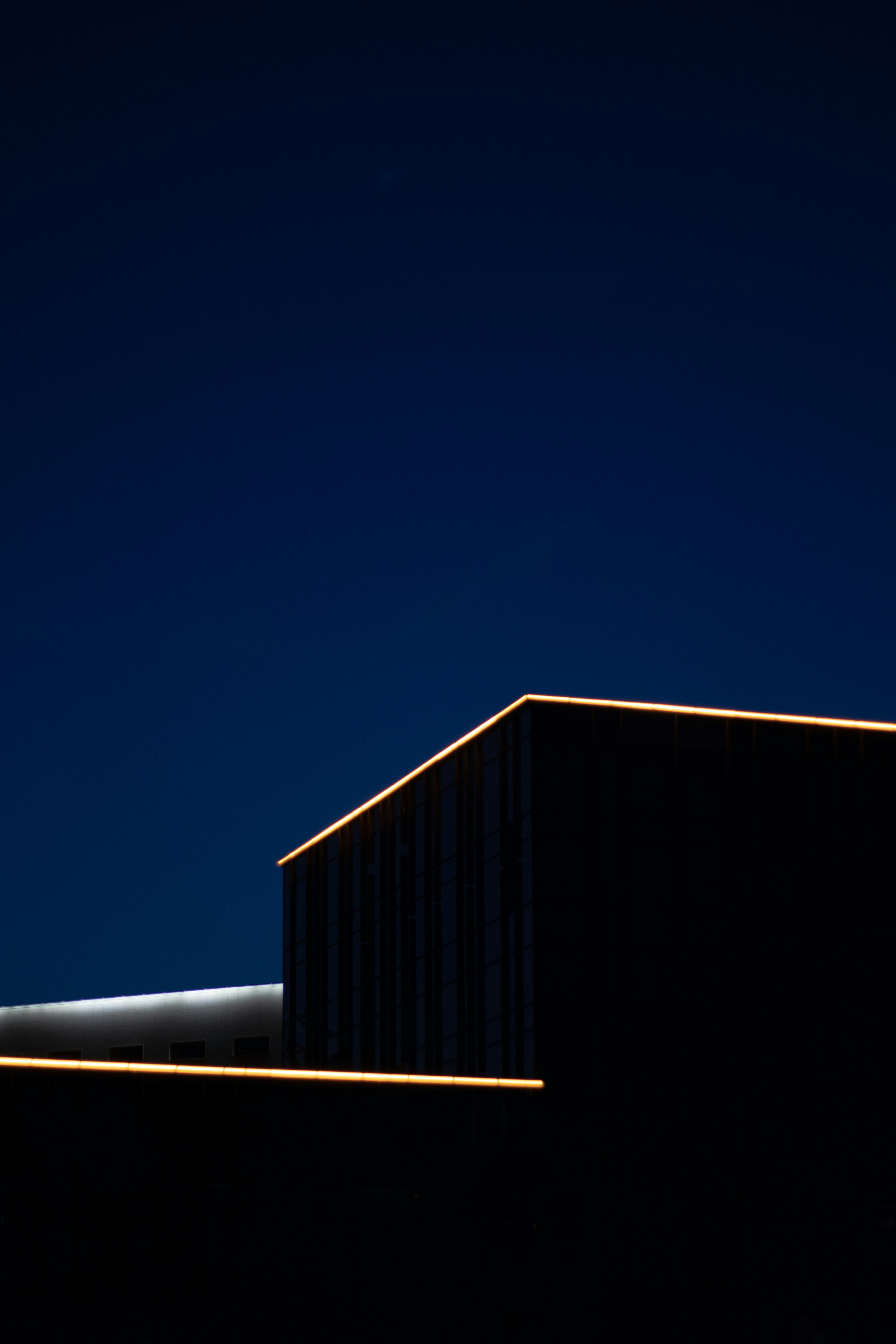 Modern building silhouette illuminated by subtle lighting against a deep blue sky.