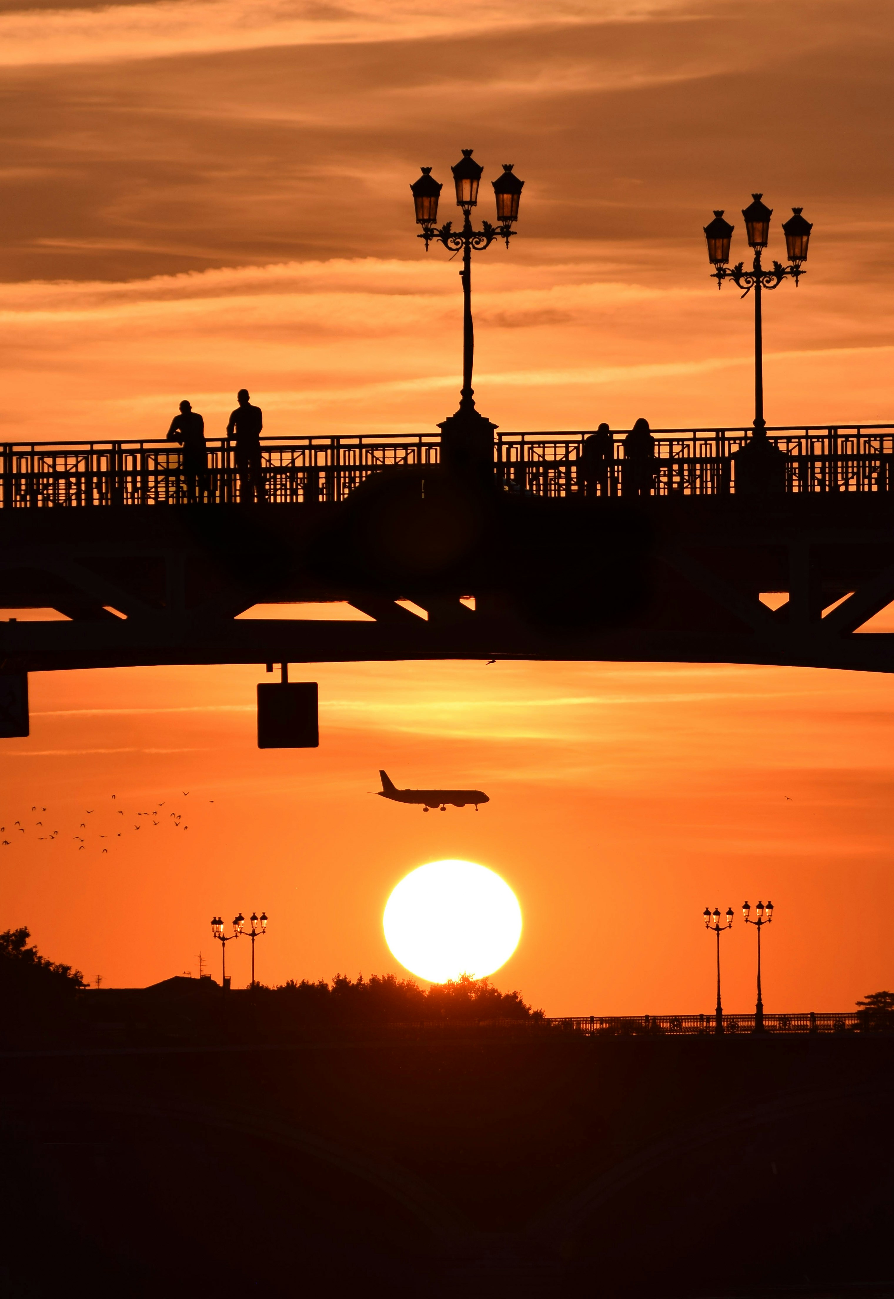 Sunset Silhouette Over Lanterned Bridge: Plane, Pedestrians, and a Fiery Horizon