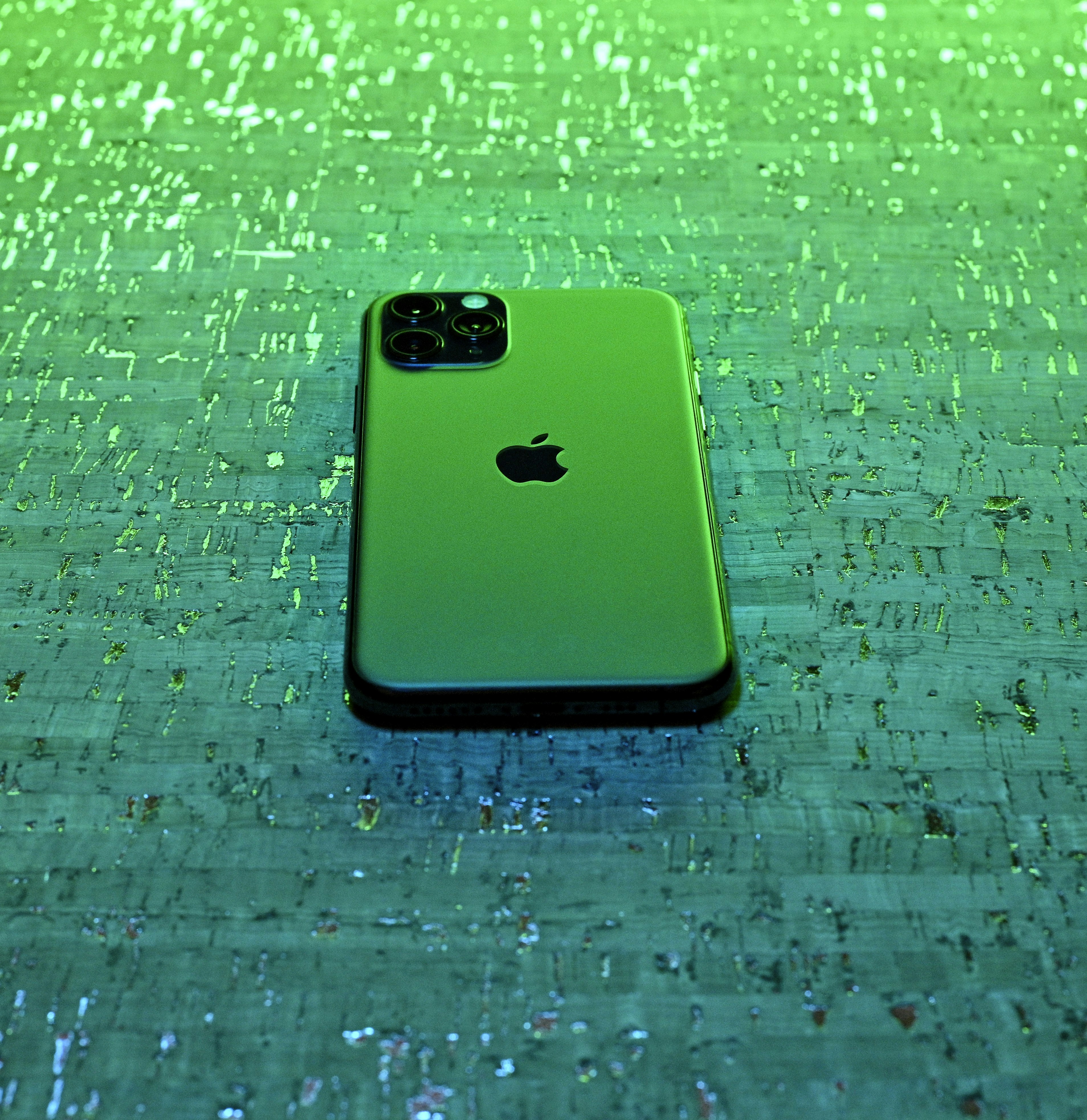 Neon Gleam: iPhone Resting on a Textured, Green-Hued Surface