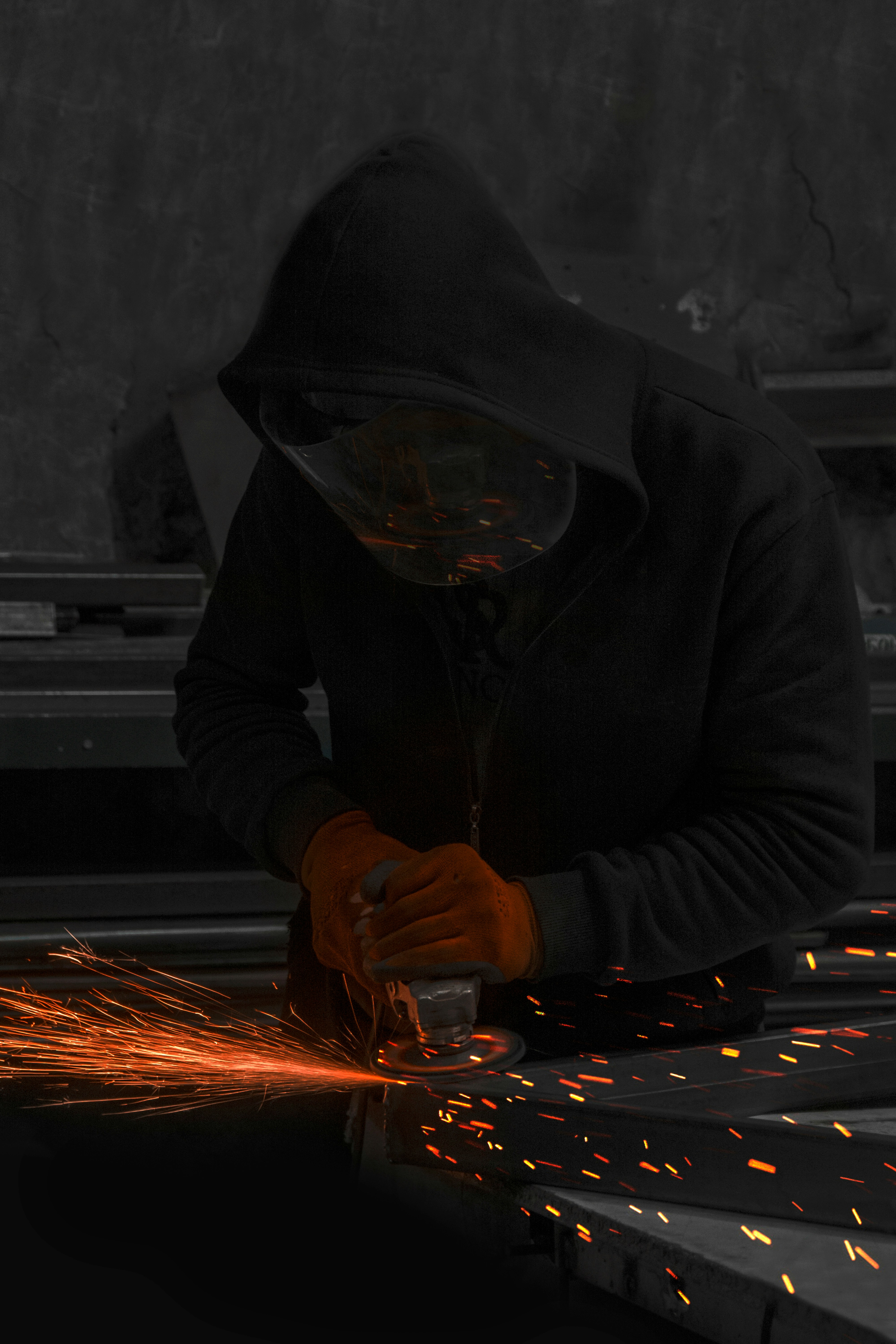 Ember Veil: A Hooded Welder Sparks in the Dim Workshop