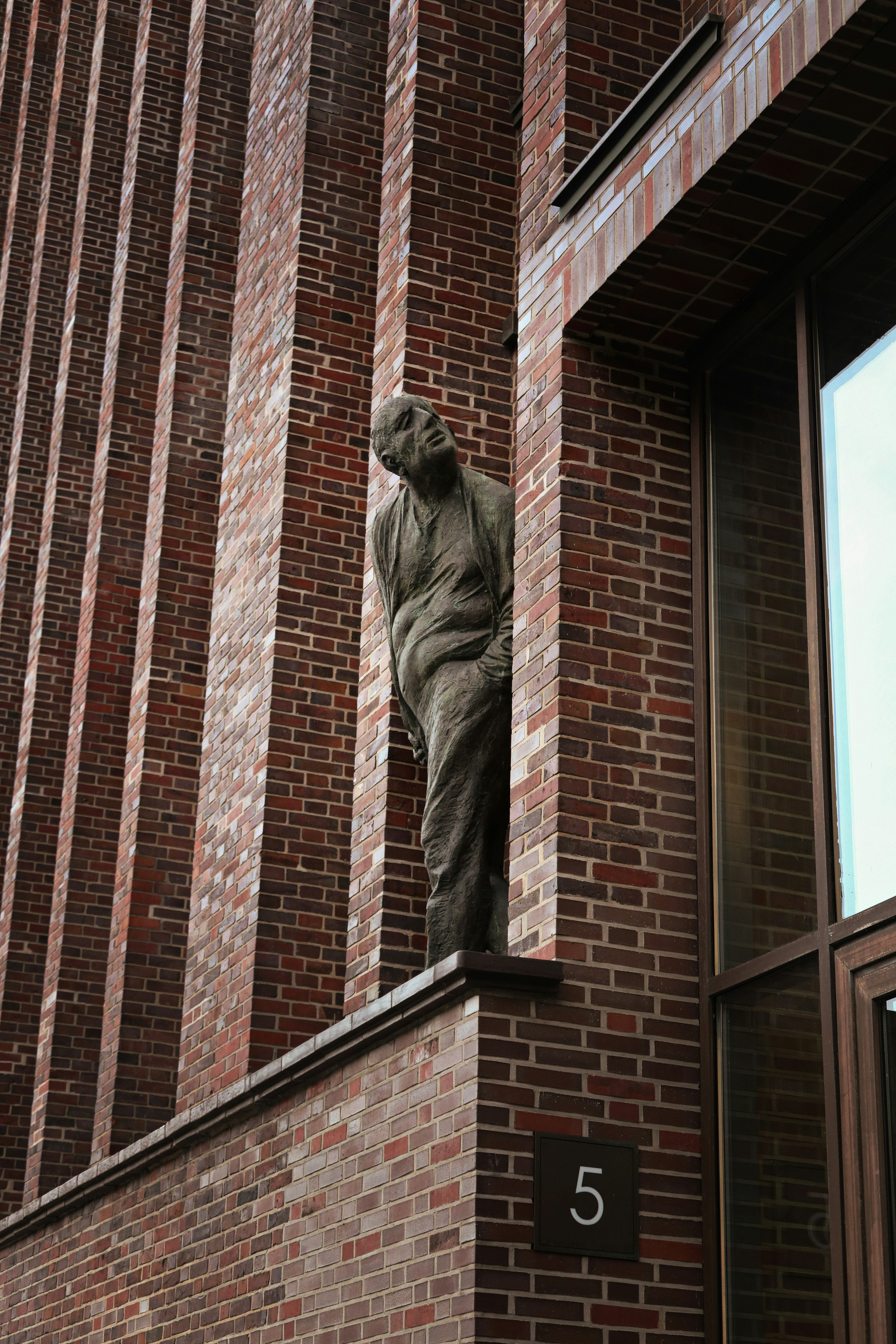 A whimsical sculpture peeks from a brick building's corner, blending art with architecture. The figure's posture adds intrigue to the urban landscape.