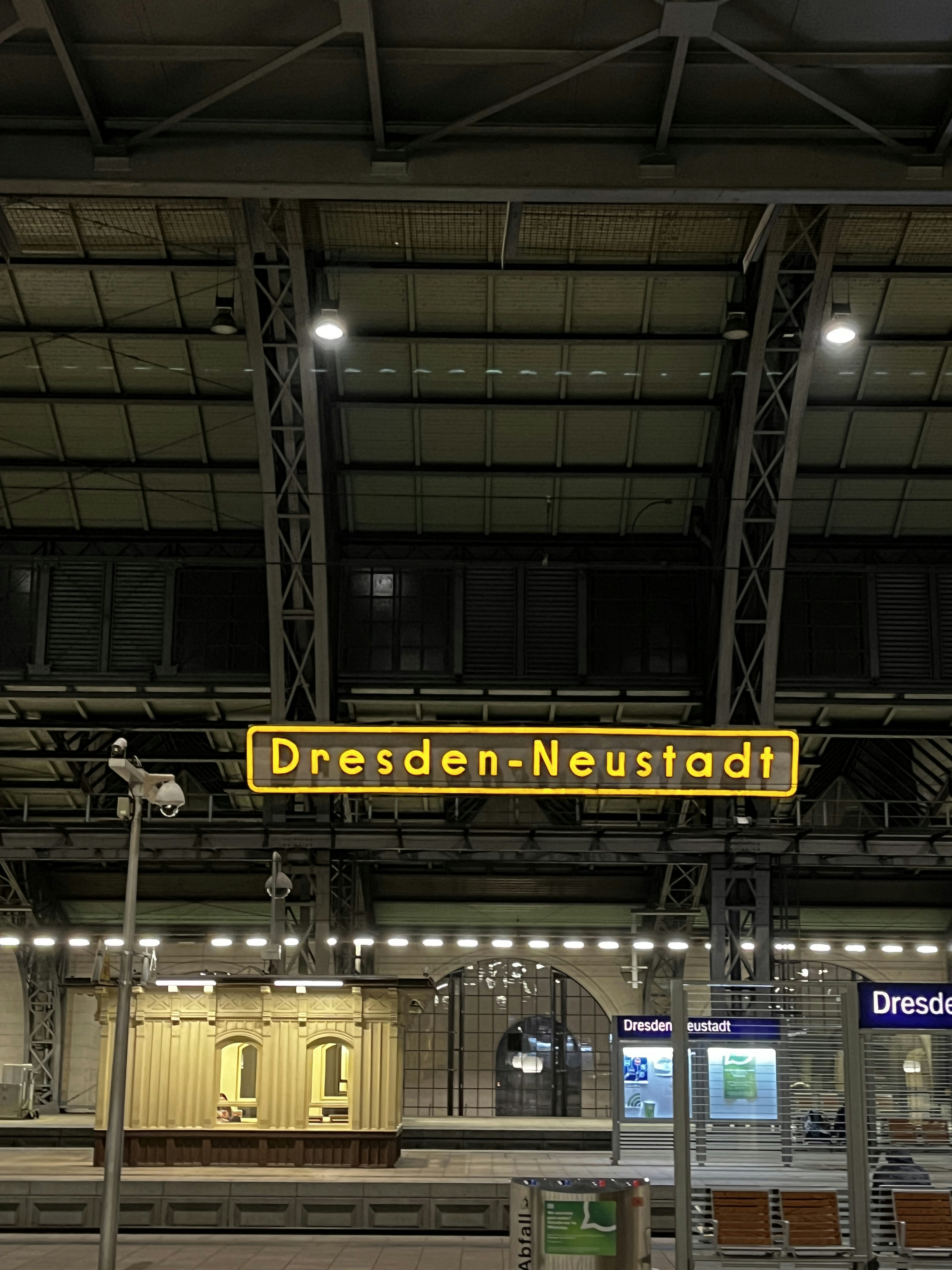 Brightly lit station sign reading 'Dresden-Neustadt' against an industrial backdrop, showcasing the essence of urban transit. The scene captures the architectural features of the station.