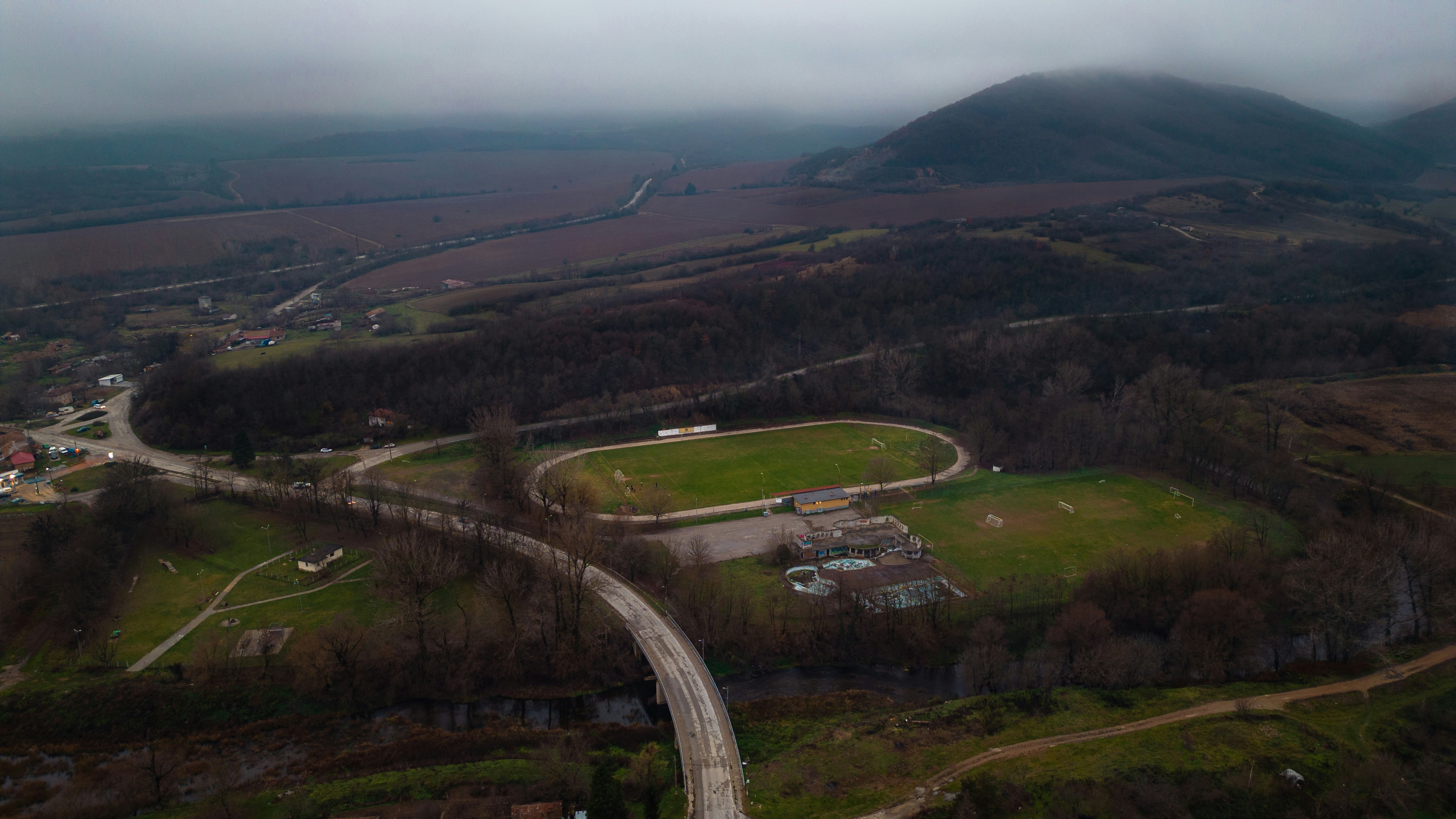 Circular Green Arena Framed by a Winding Road Beneath a Cloudy Park Horizon