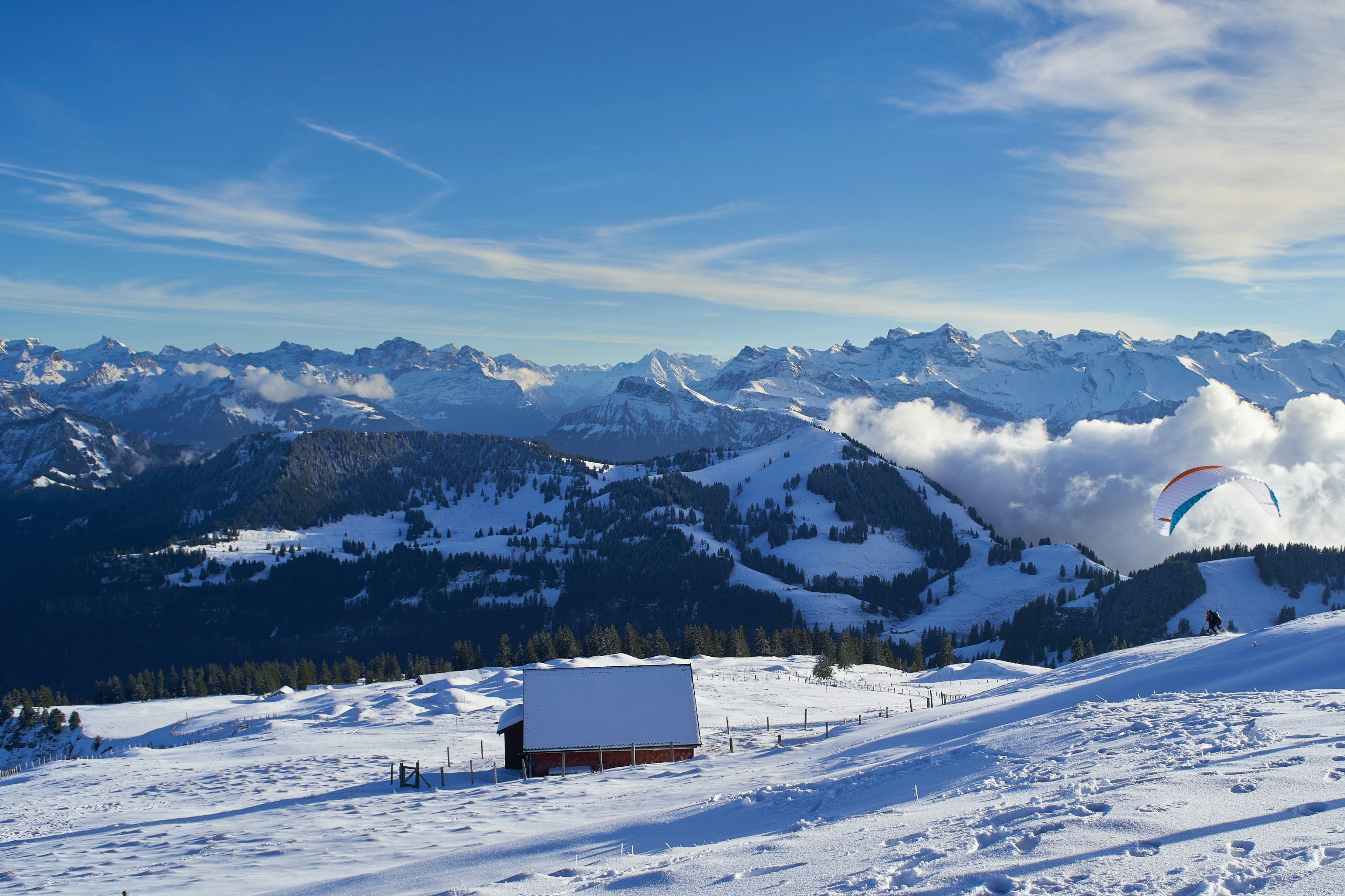 Snowbound Chalet Beneath the Alpine Crest as a Paraglider Traverses the Sky