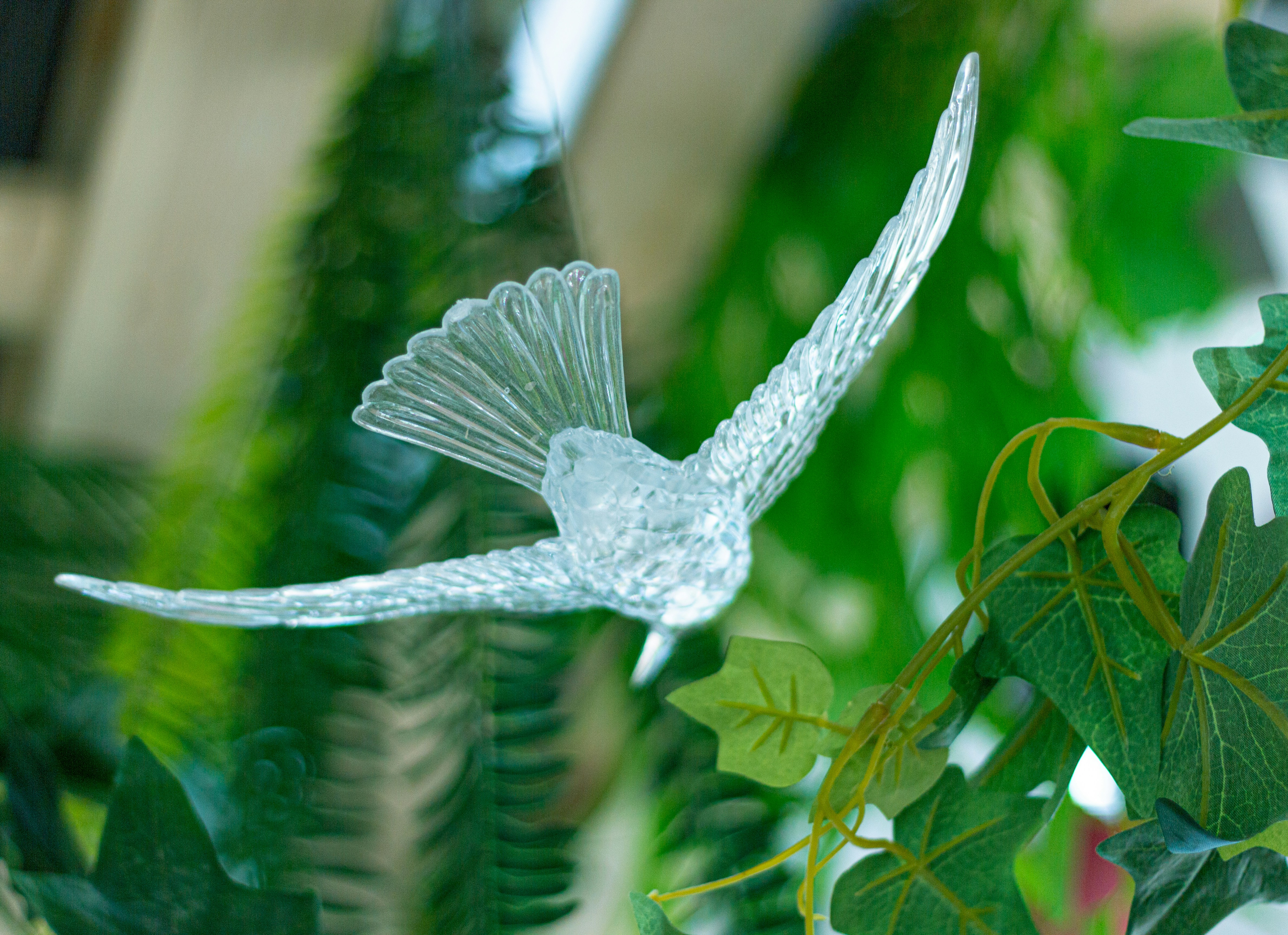 A delicate crystal bird in mid-flight, surrounded by lush green foliage, capturing a moment of elegance and tranquility.