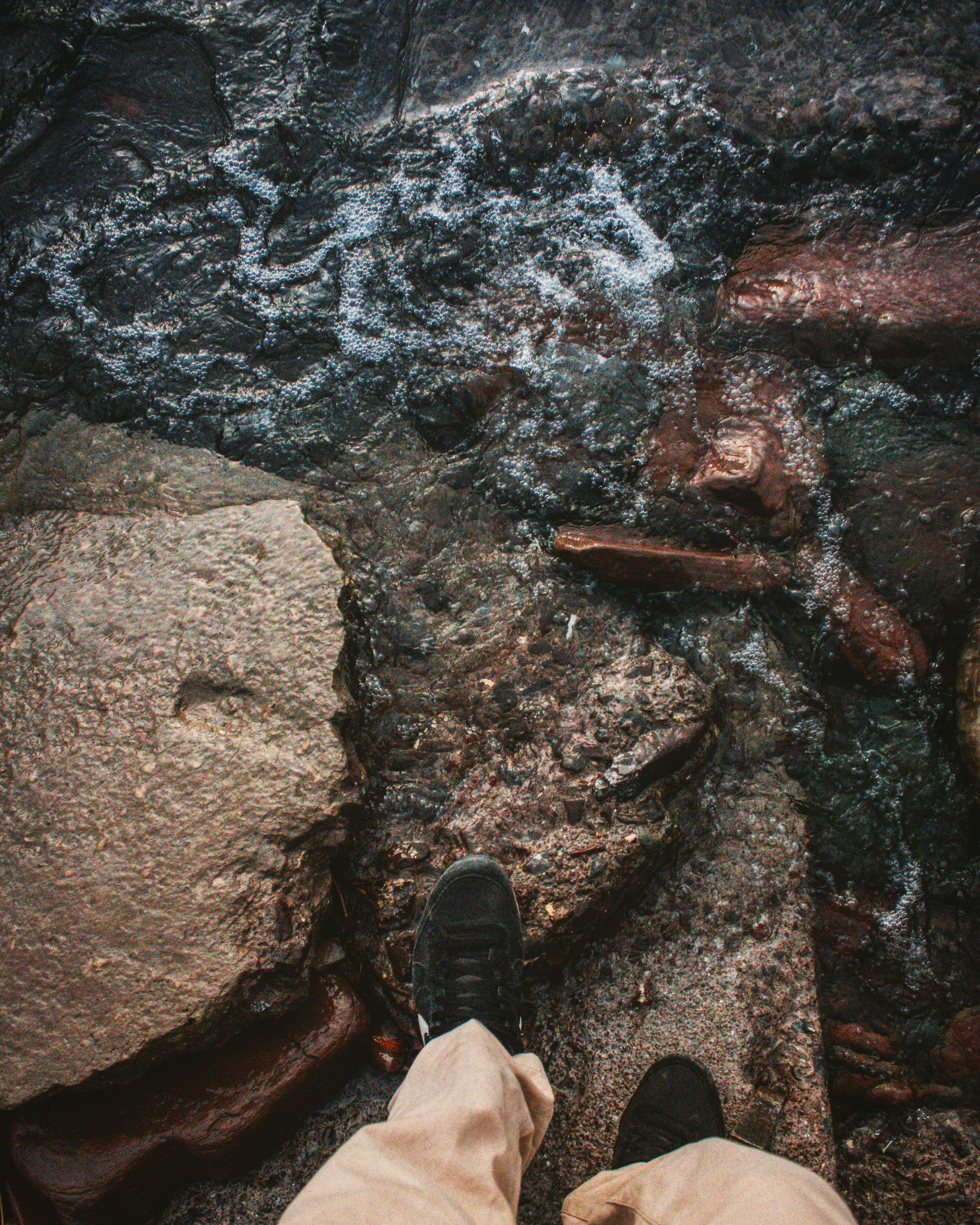 A lone sneaker steps along rain-slick lava rock by the shore