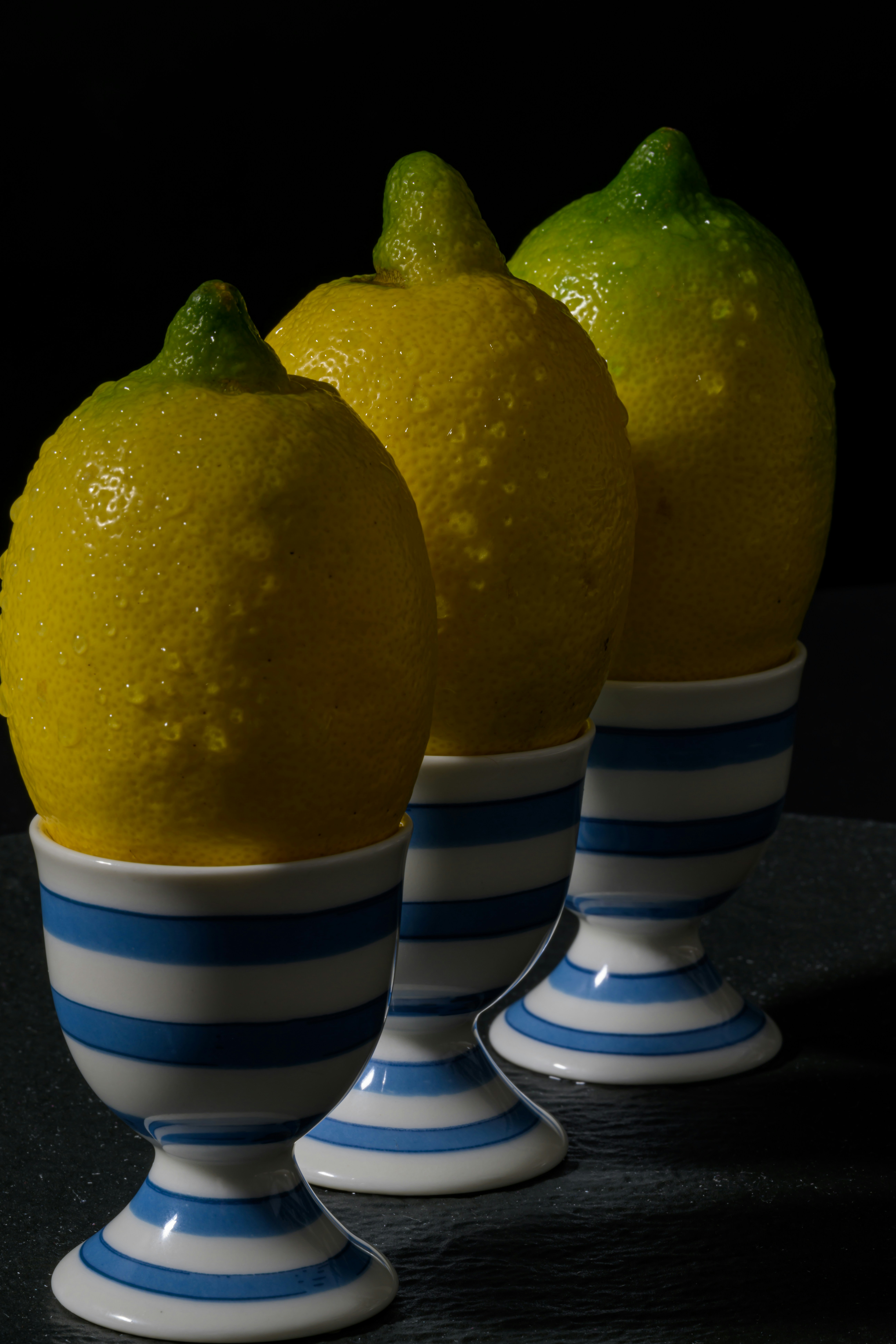 Three lemons perched in striped egg cups against a dark background, showcasing their vibrant color and texture.