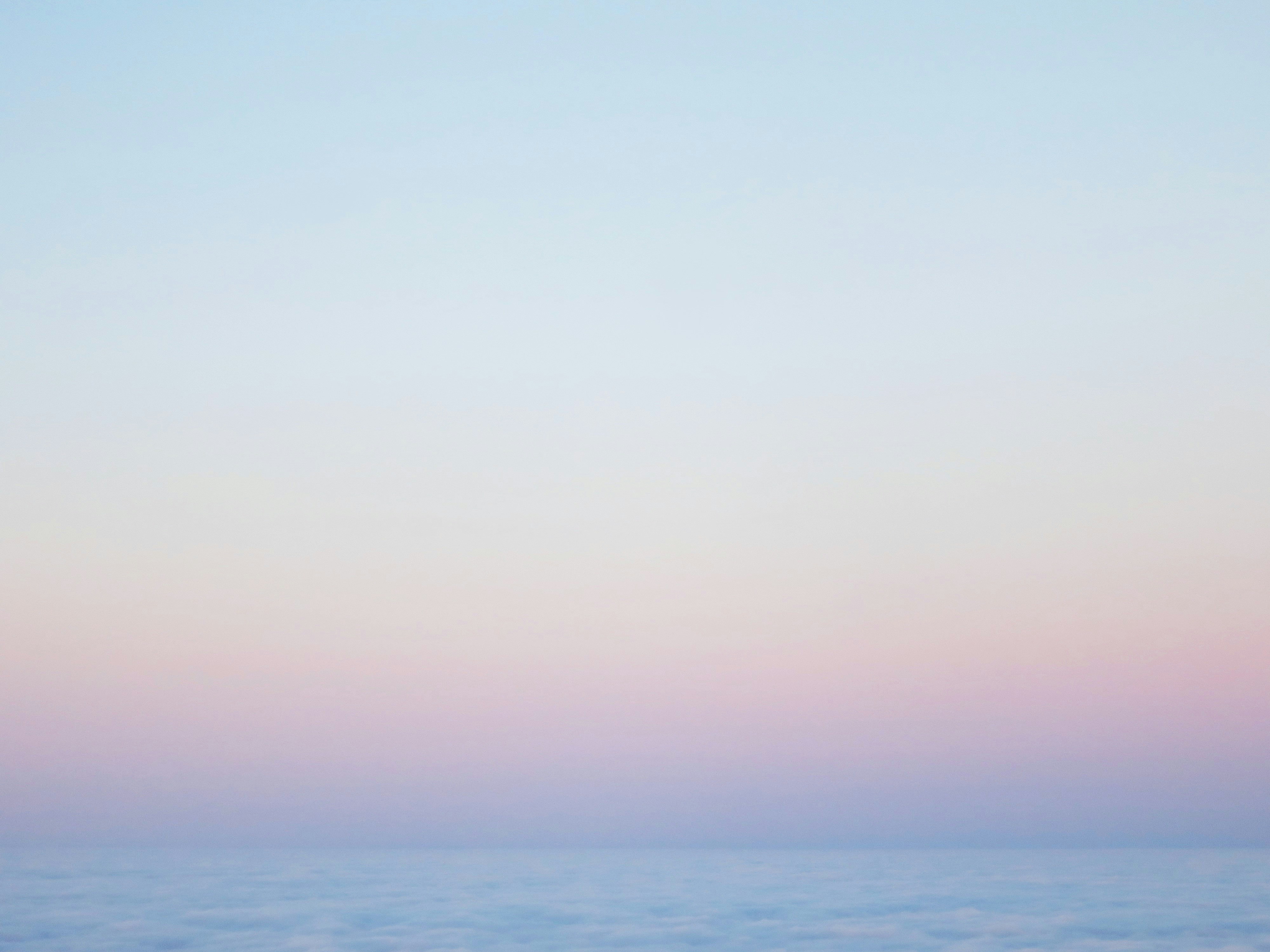 Soft pastel hues blend seamlessly in the sky above a calm ocean, evoking a sense of peace and serenity.