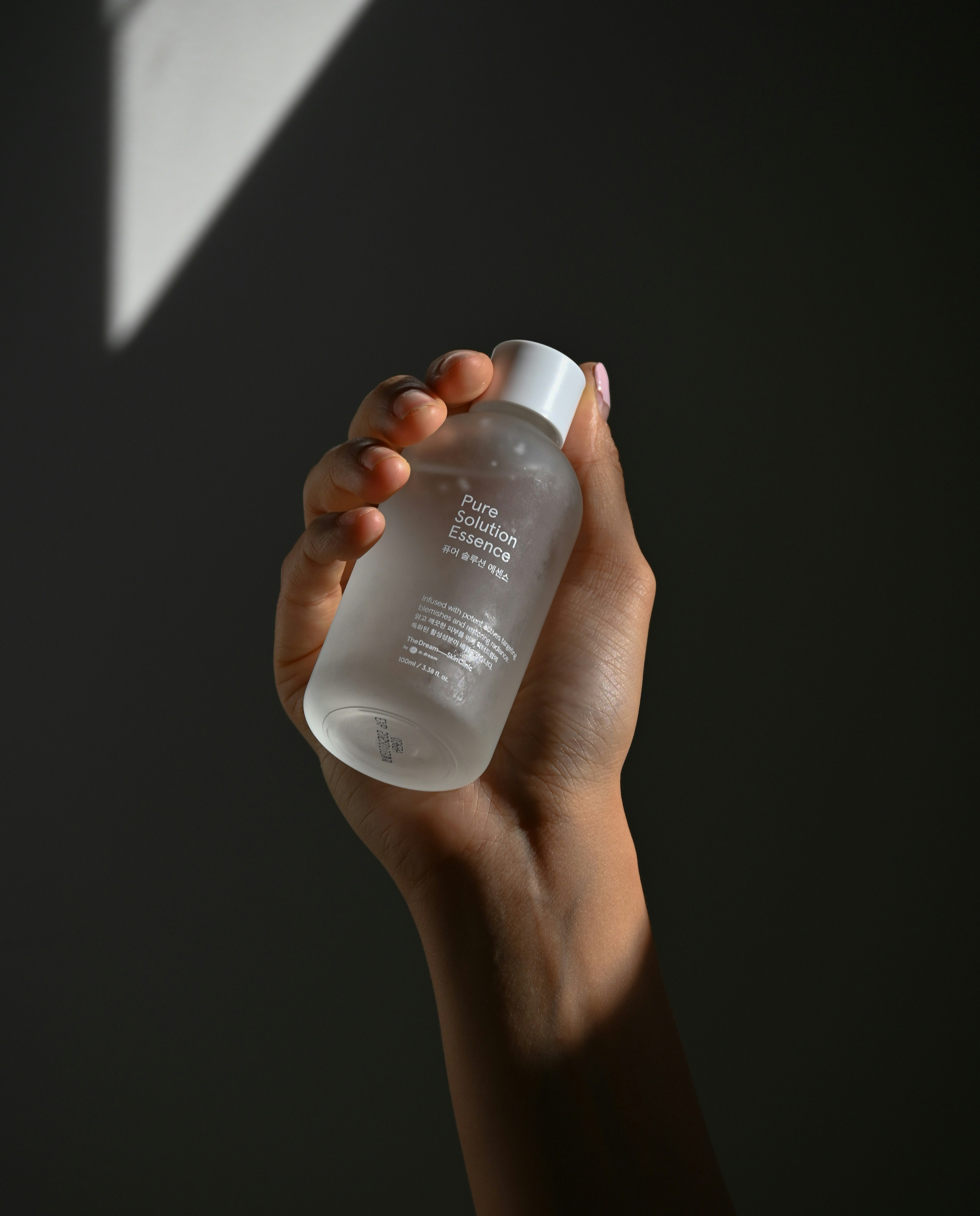 Hand holding a translucent bottle of essence, illuminated by soft light against a dark background.
