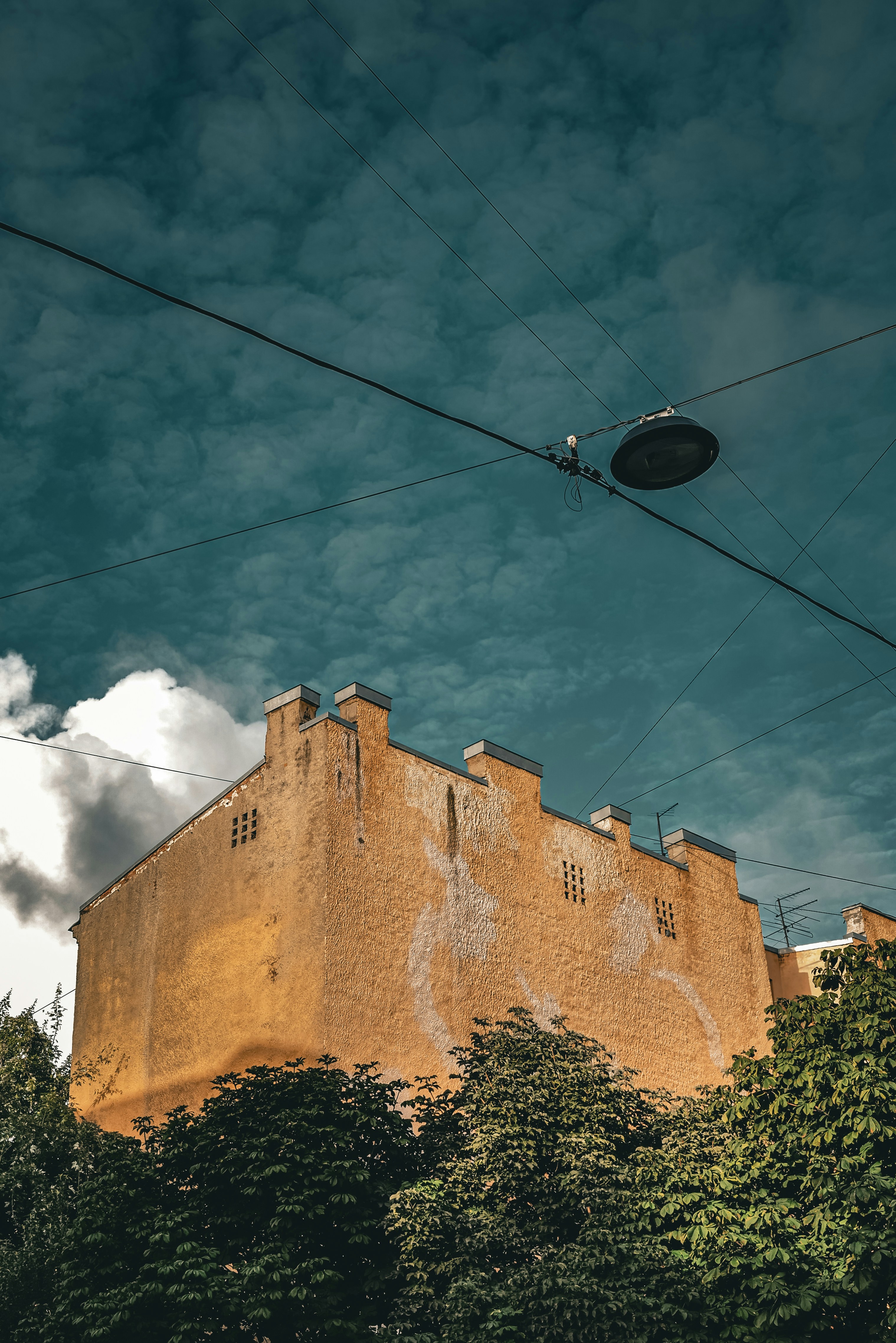 Urban Castle Under Cables: A Cracked Sunlit Facade Beneath a Looming Street Lamp