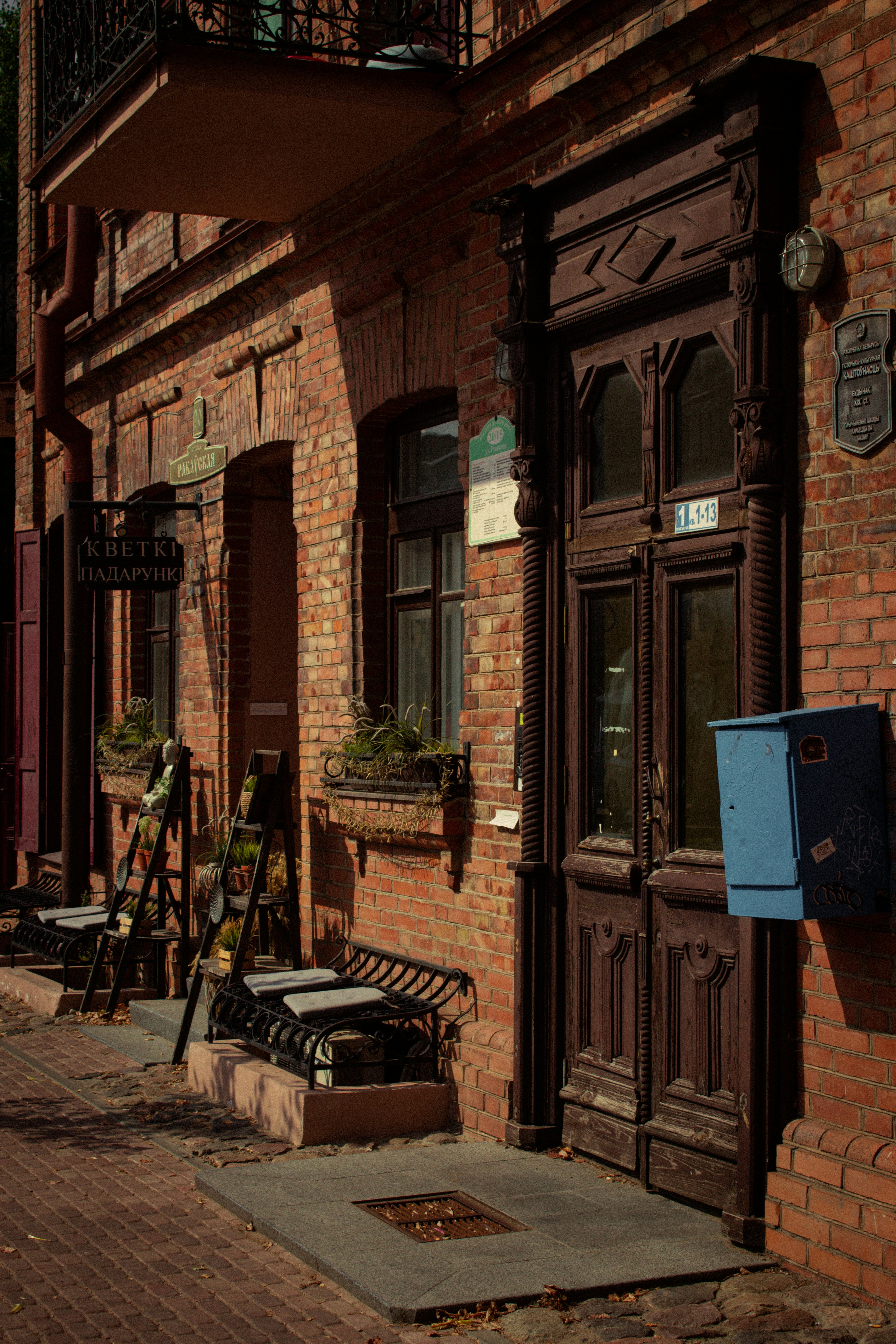 Charming brick facade showcasing a vintage door, window boxes, and rustic seating, illuminated by warm sunlight. A blue mailbox adds a pop of color to the scene.