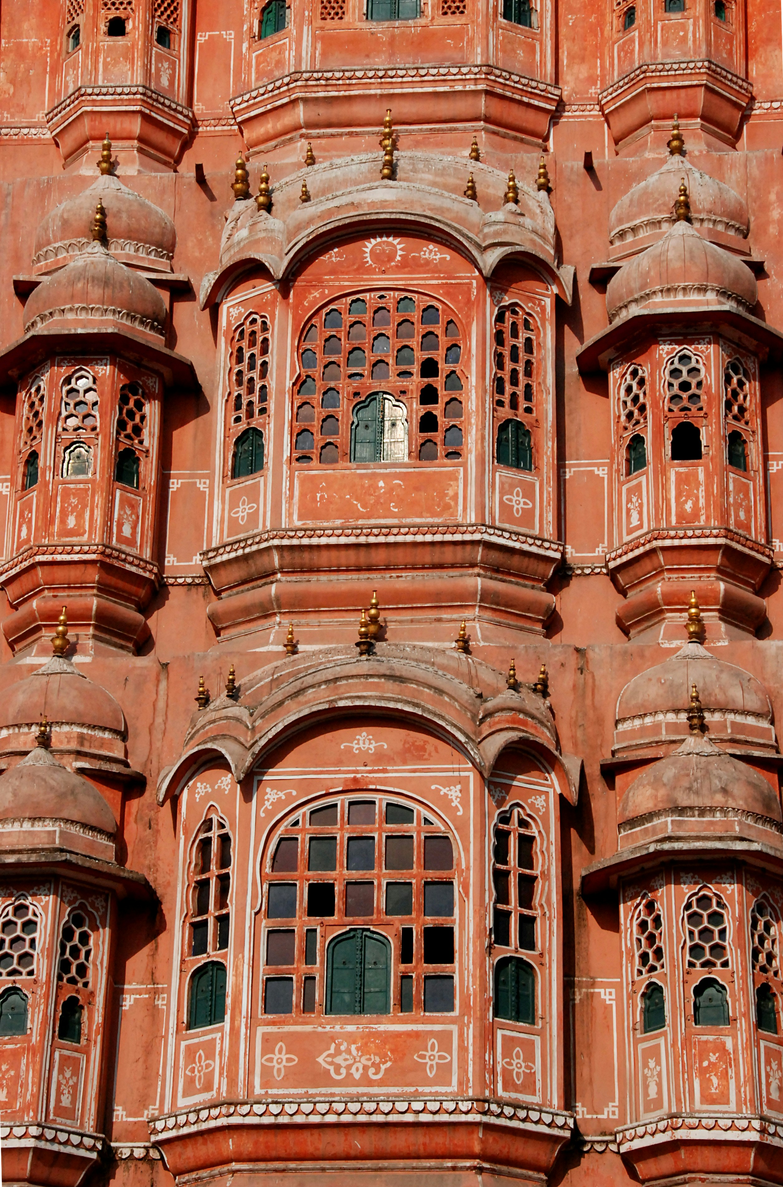 Intricate windows and domes of a historic palace exhibit traditional Indian architectural design. The warm hues of the façade highlight the craftsmanship.