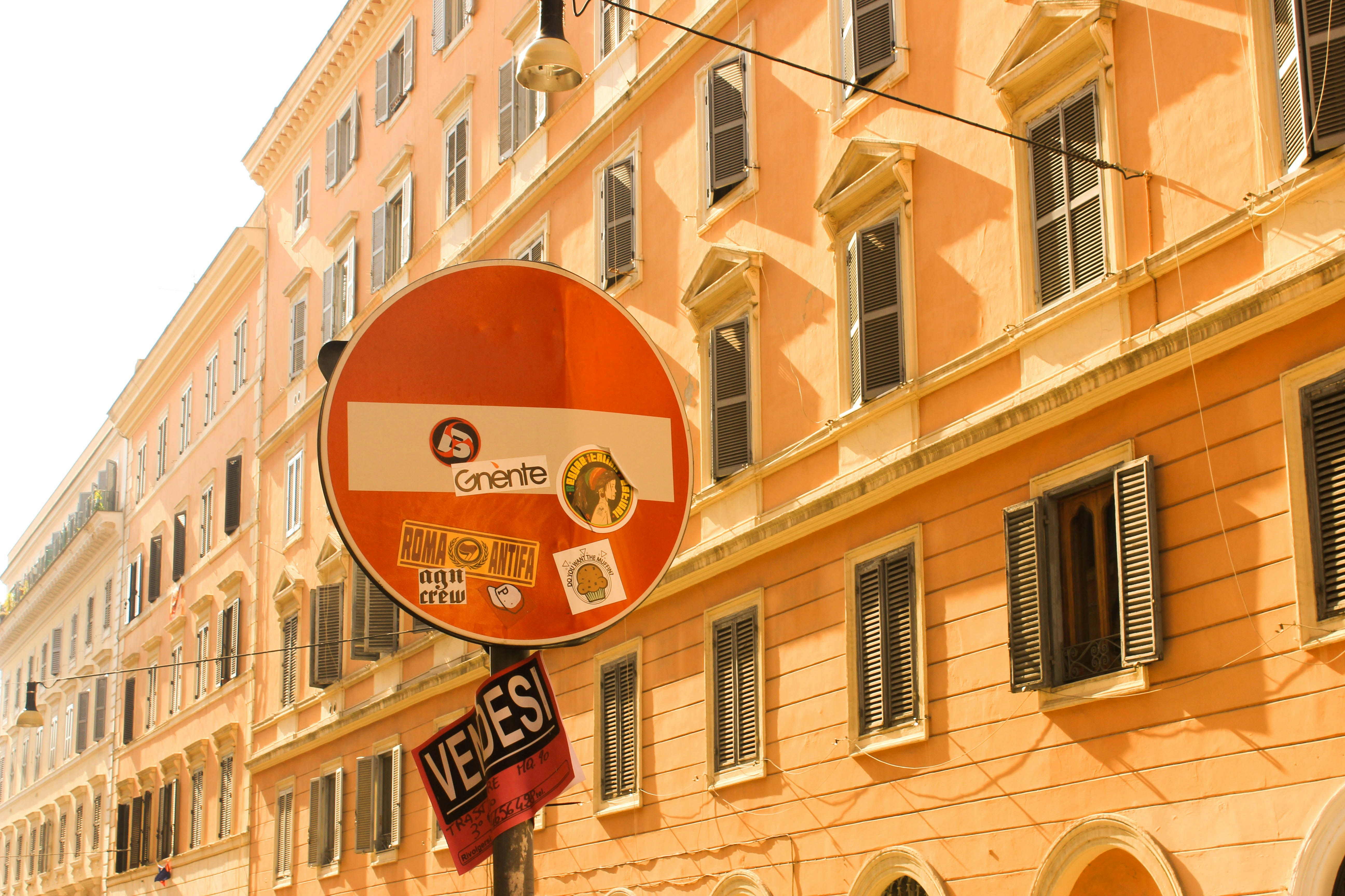 Stickered No-Entry Sign Anchored by a Sunlit Orange Facade