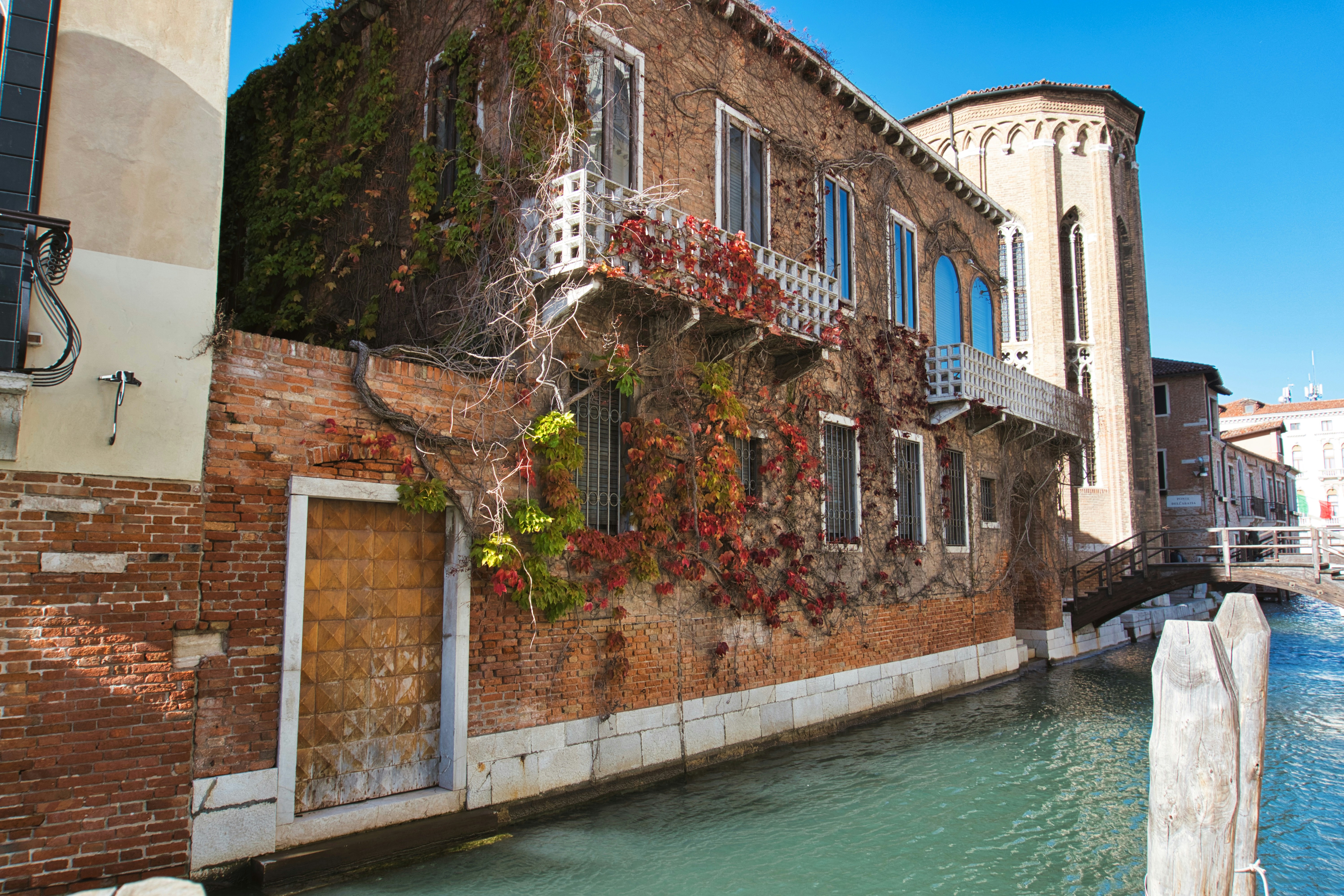 Brick building with ivy-covered facade beside a tranquil canal under a clear blue sky.