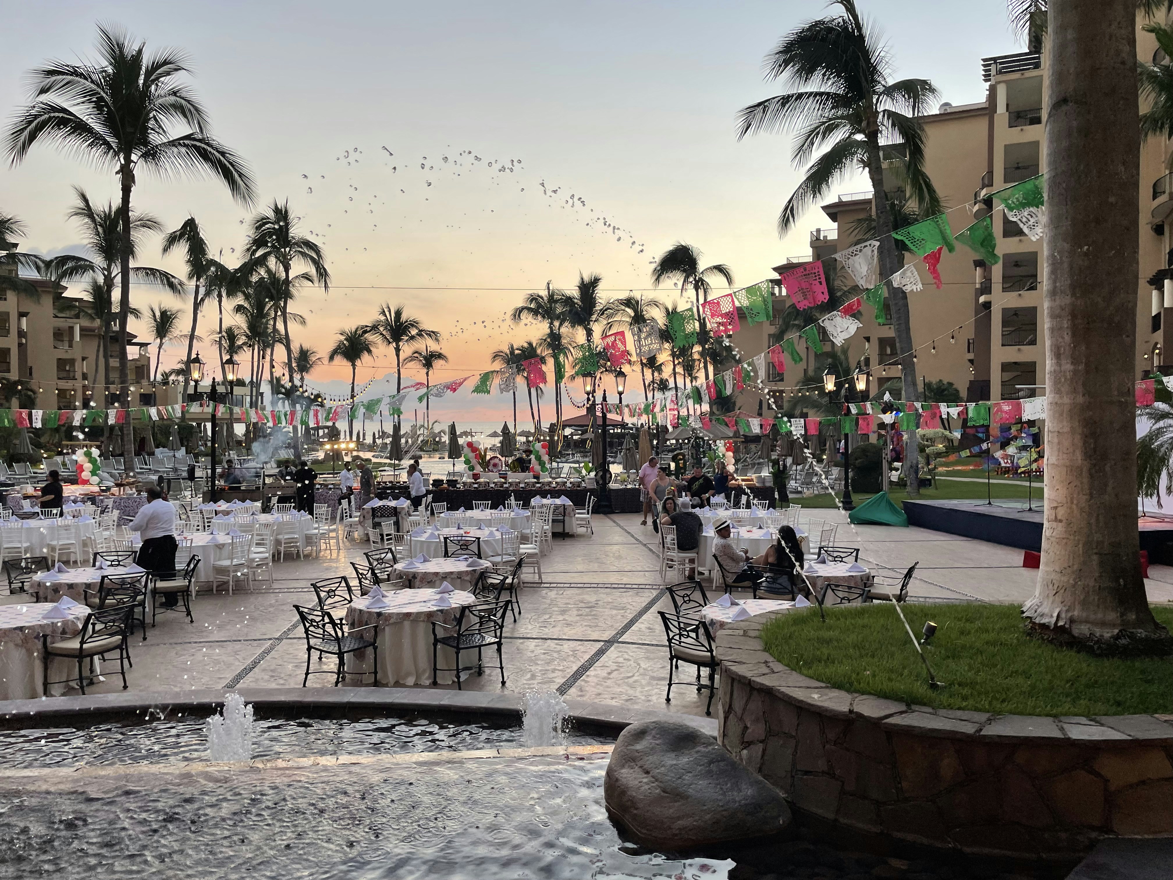 Outdoor dining setup with festive decorations at a seaside resort during sunset.
