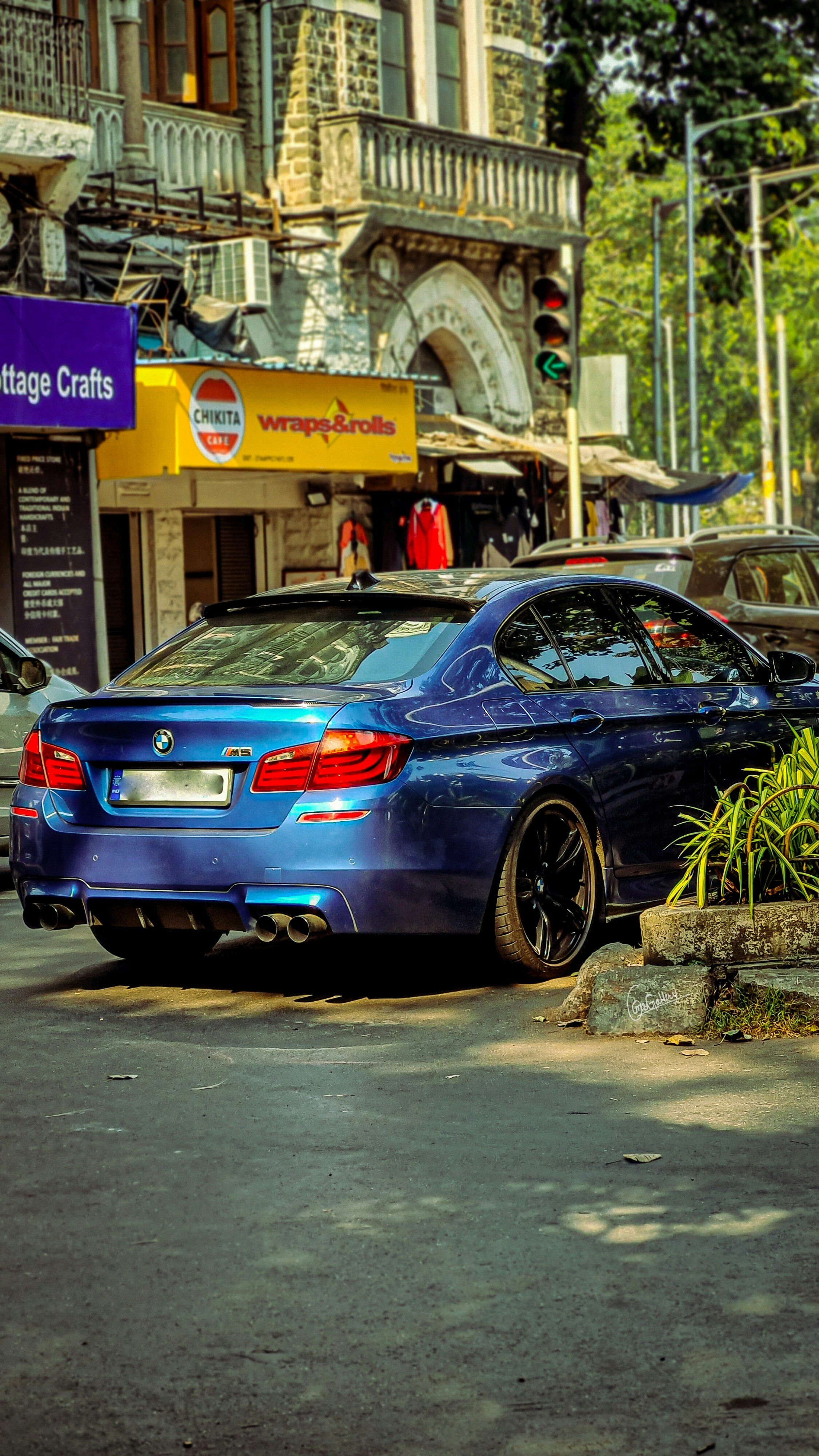 A sleek blue BMW M5 parked beside vibrant storefronts in a bustling urban environment.
