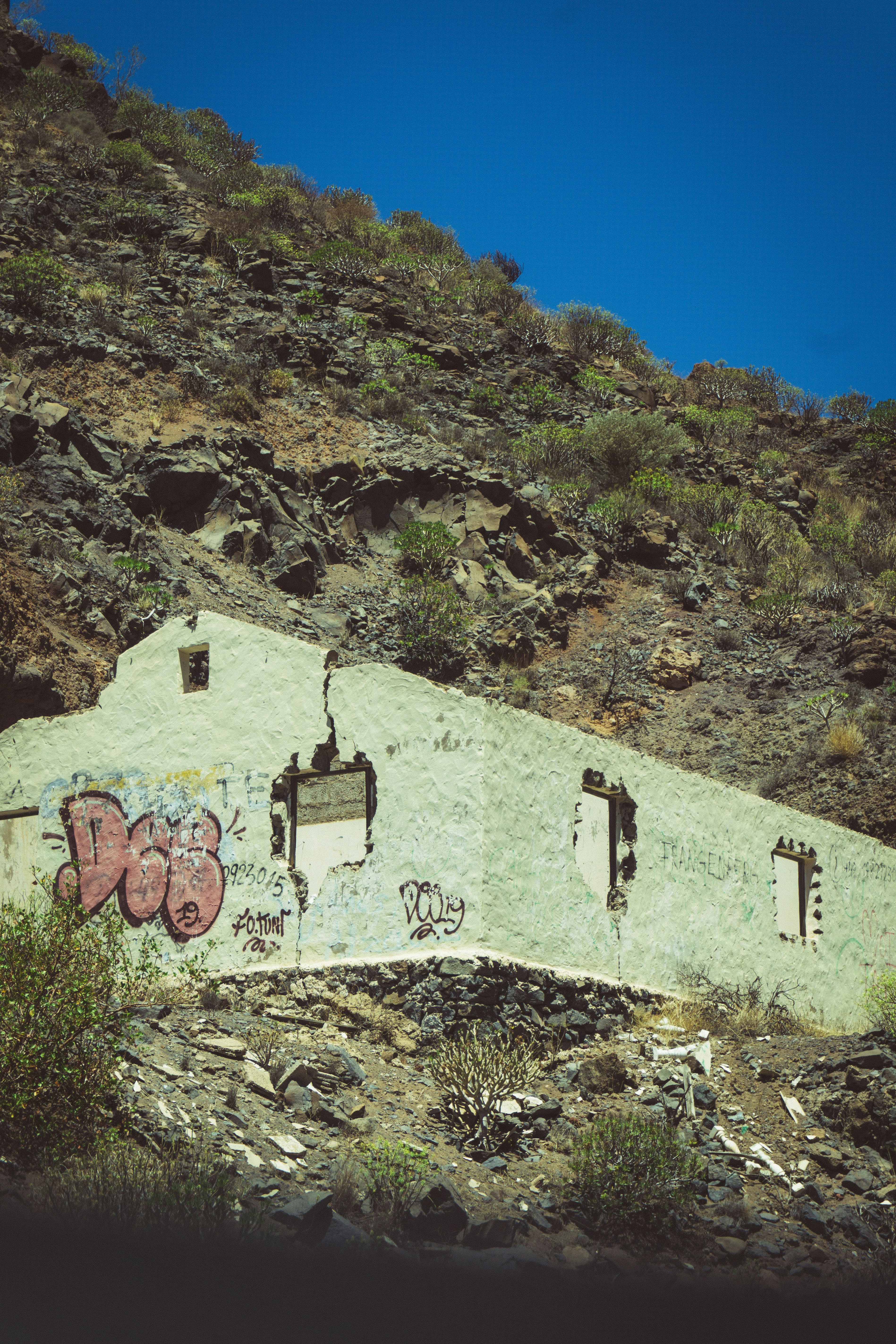 Ruined hillside shelter: graffiti-clad concrete shell beneath a sunlit cliff