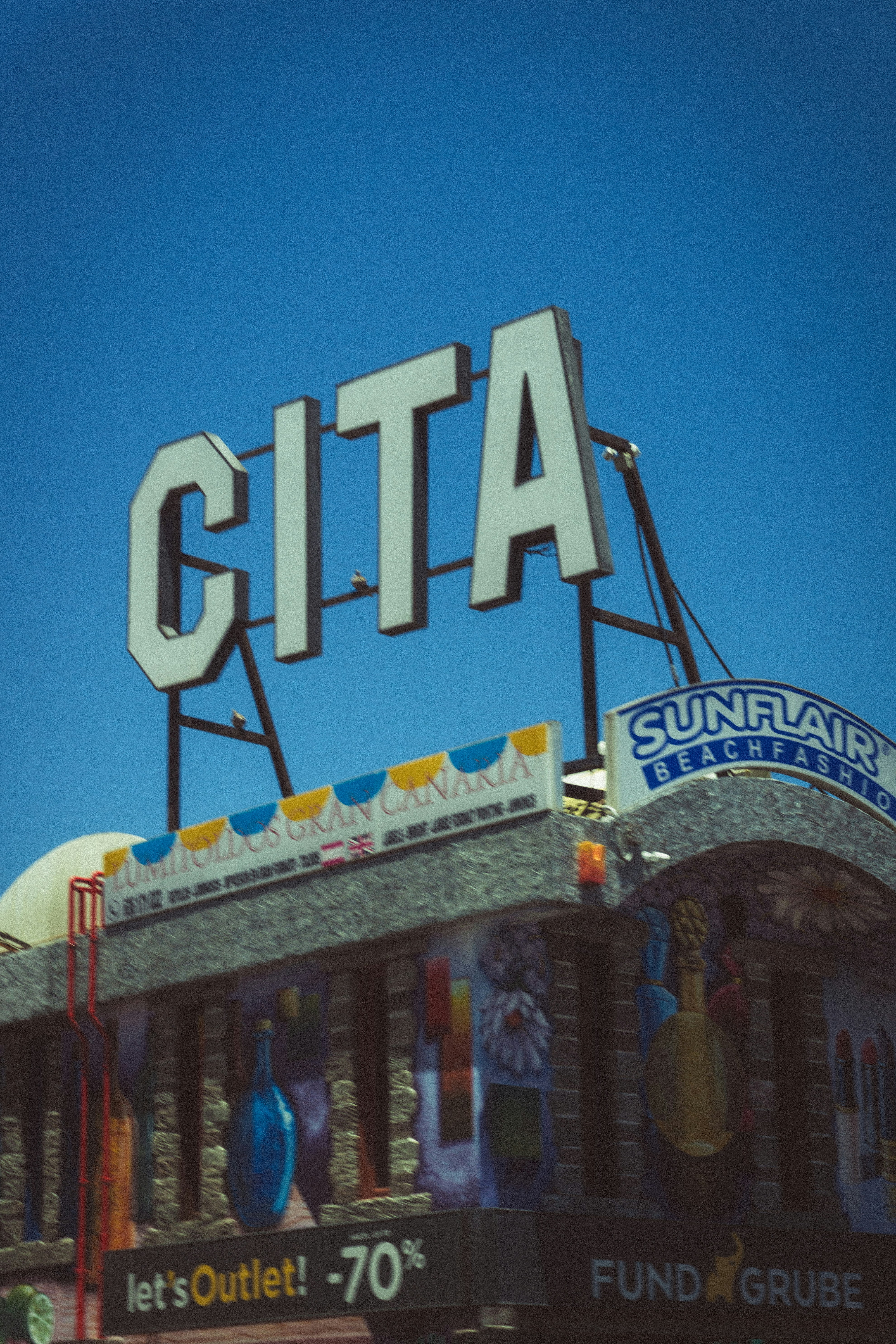 Bold GITA letters rise above a weathered beachfront building adorned with murals and promotional banners.