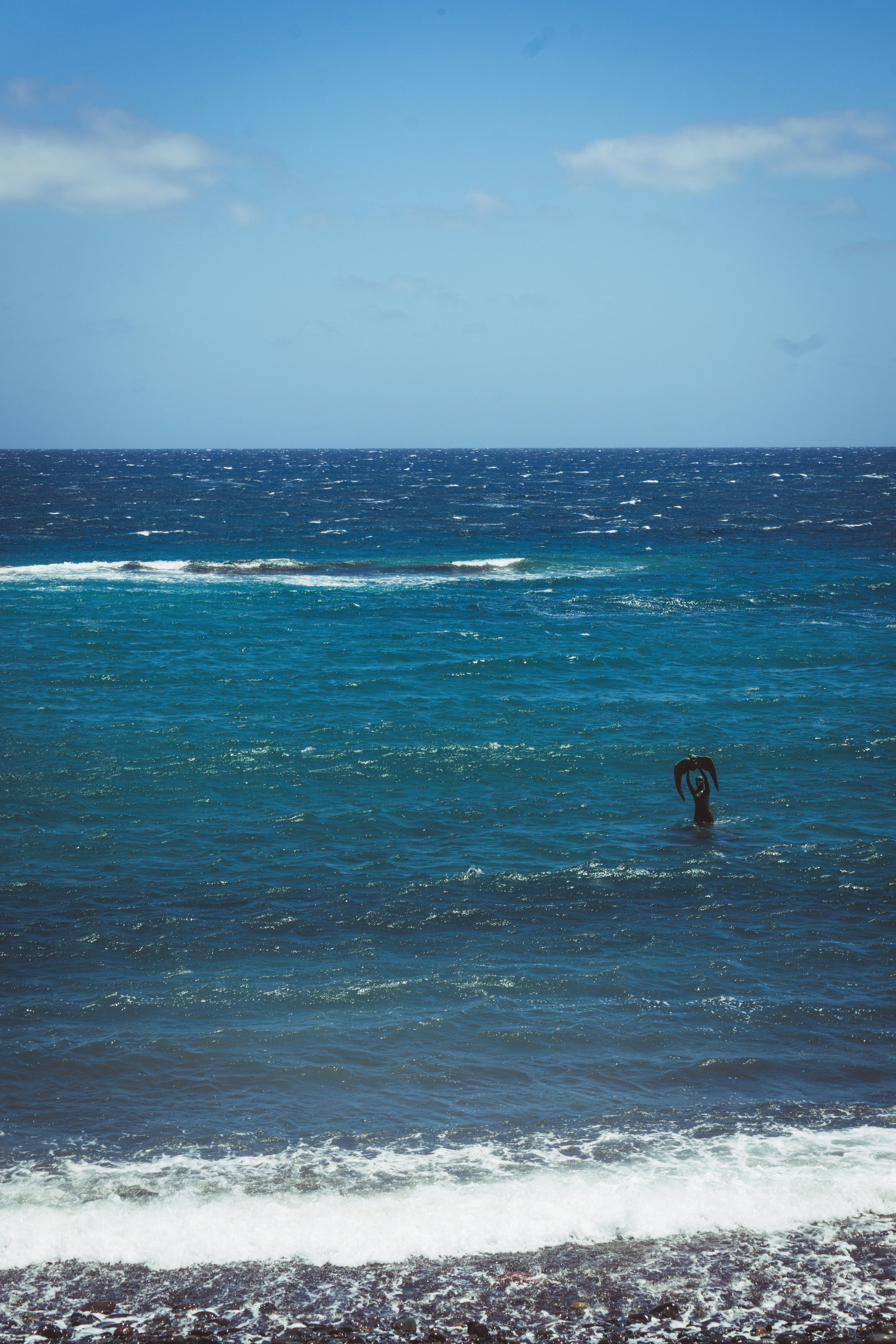 Lone Figure Rising from the Turquoise Sea Under a Wide Blue Sky