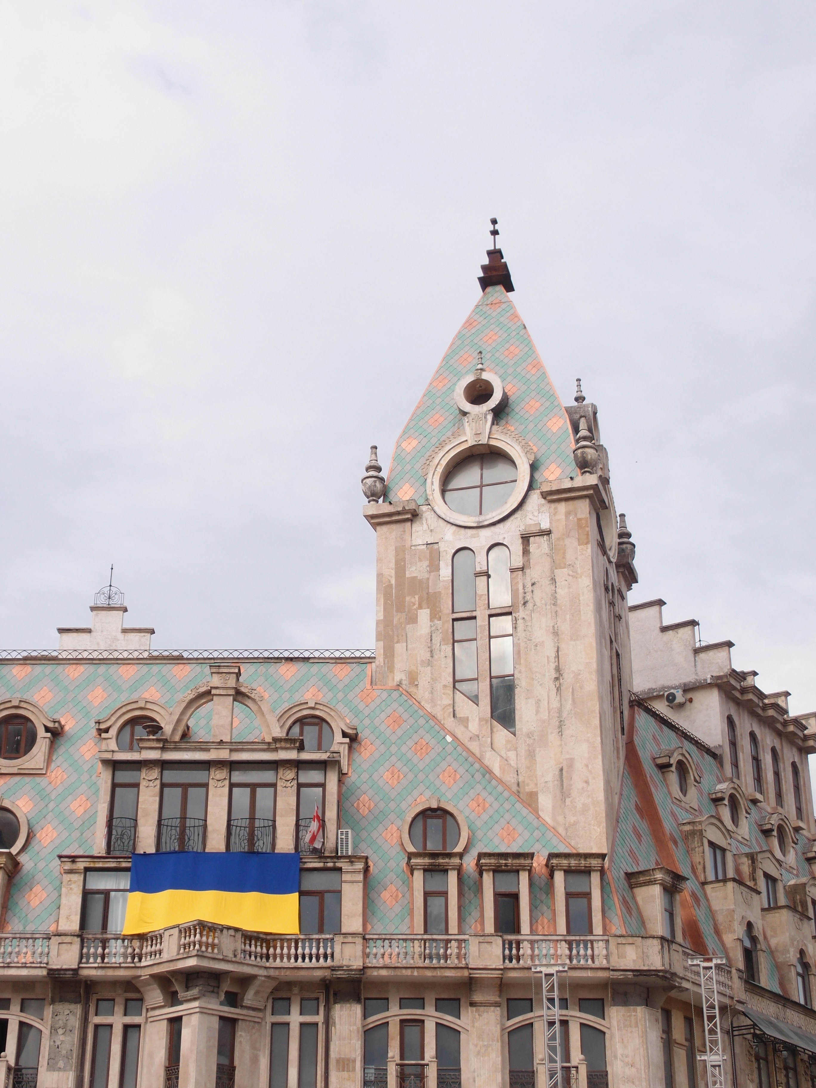 Historic building with turquoise tiled roof and ornate stonework, Ukrainian flag draped over a balcony.