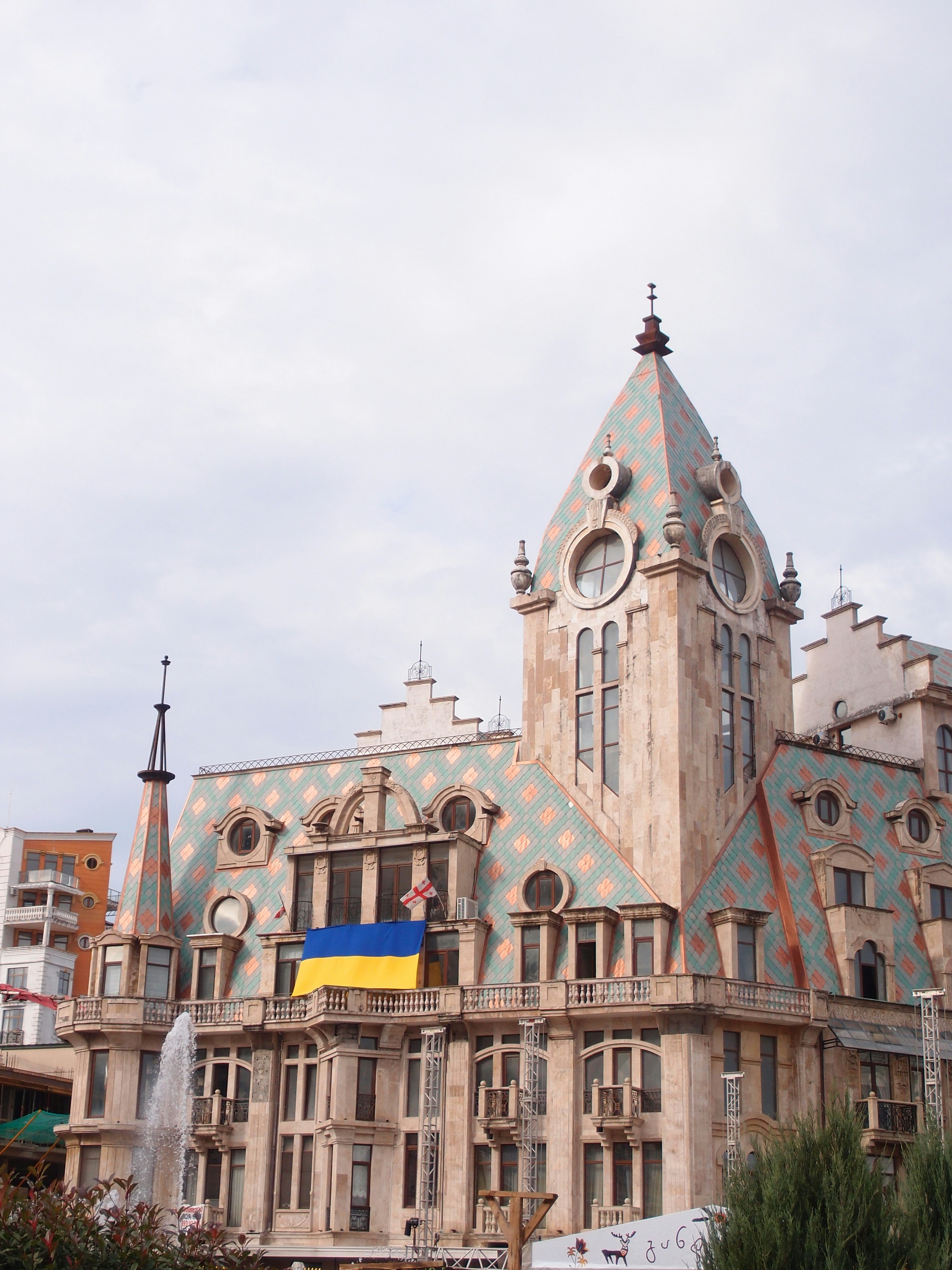 Pastel turquoise-tiled neo-Gothic city hall with ornate windows and a blue-and-yellow Ukrainian flag draped from the balcony.