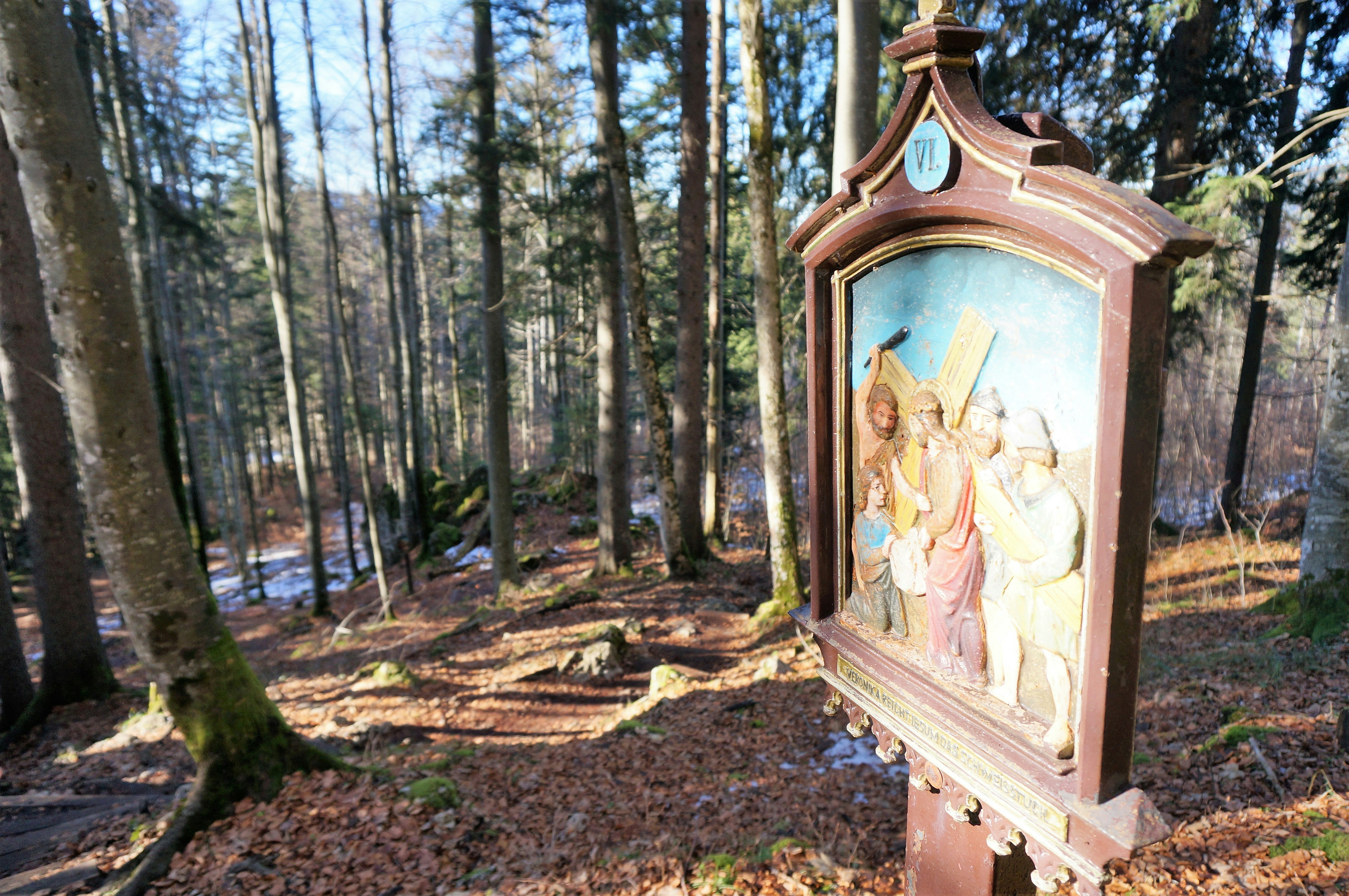 Wooden religious plaque depicting a scene of people carrying a cross, set against a backdrop of a serene forest with autumn foliage.
