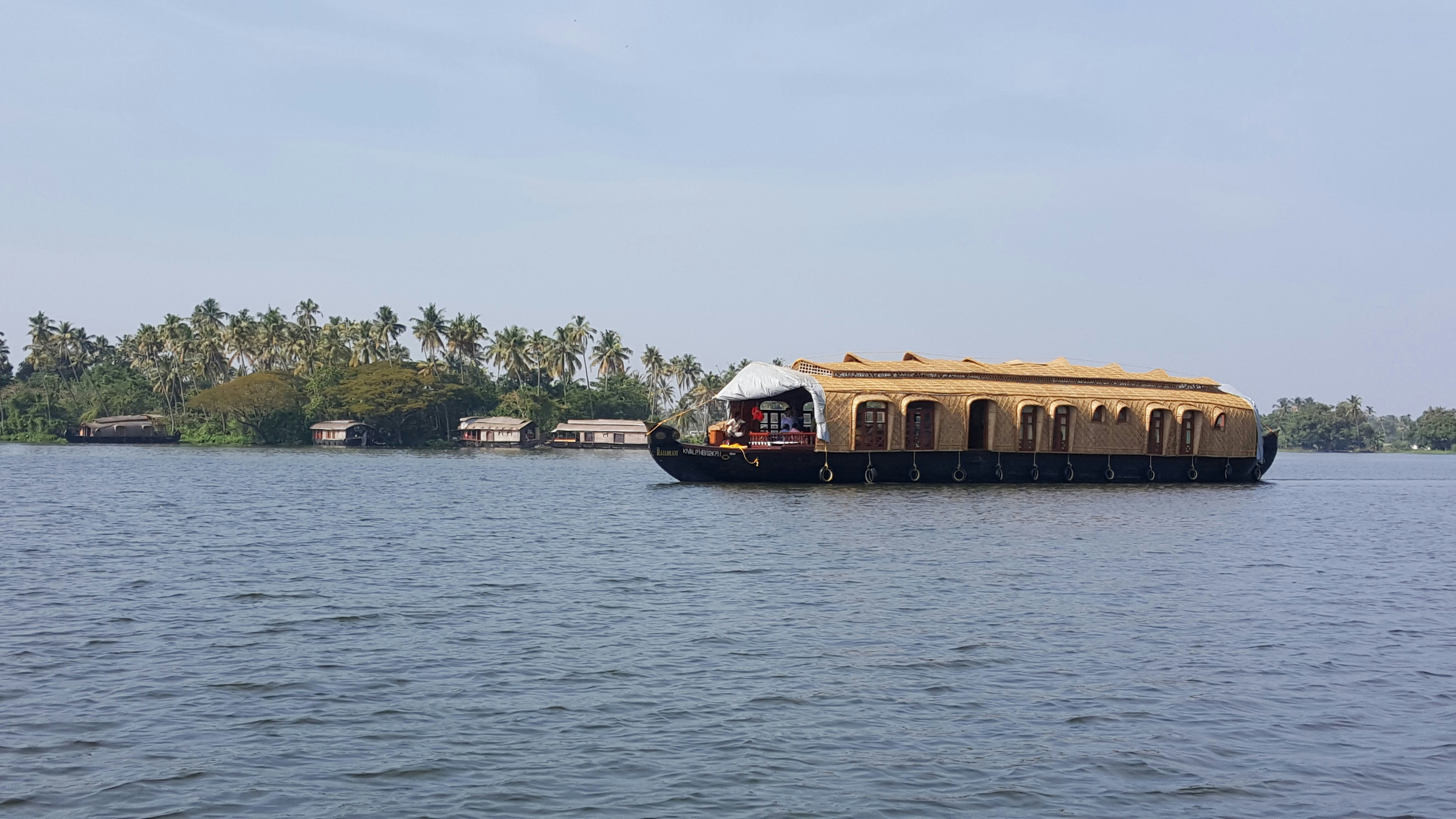 Traditional houseboat gliding through calm waters with lush greenery in the background. The scene captures the essence of tranquil waterways.