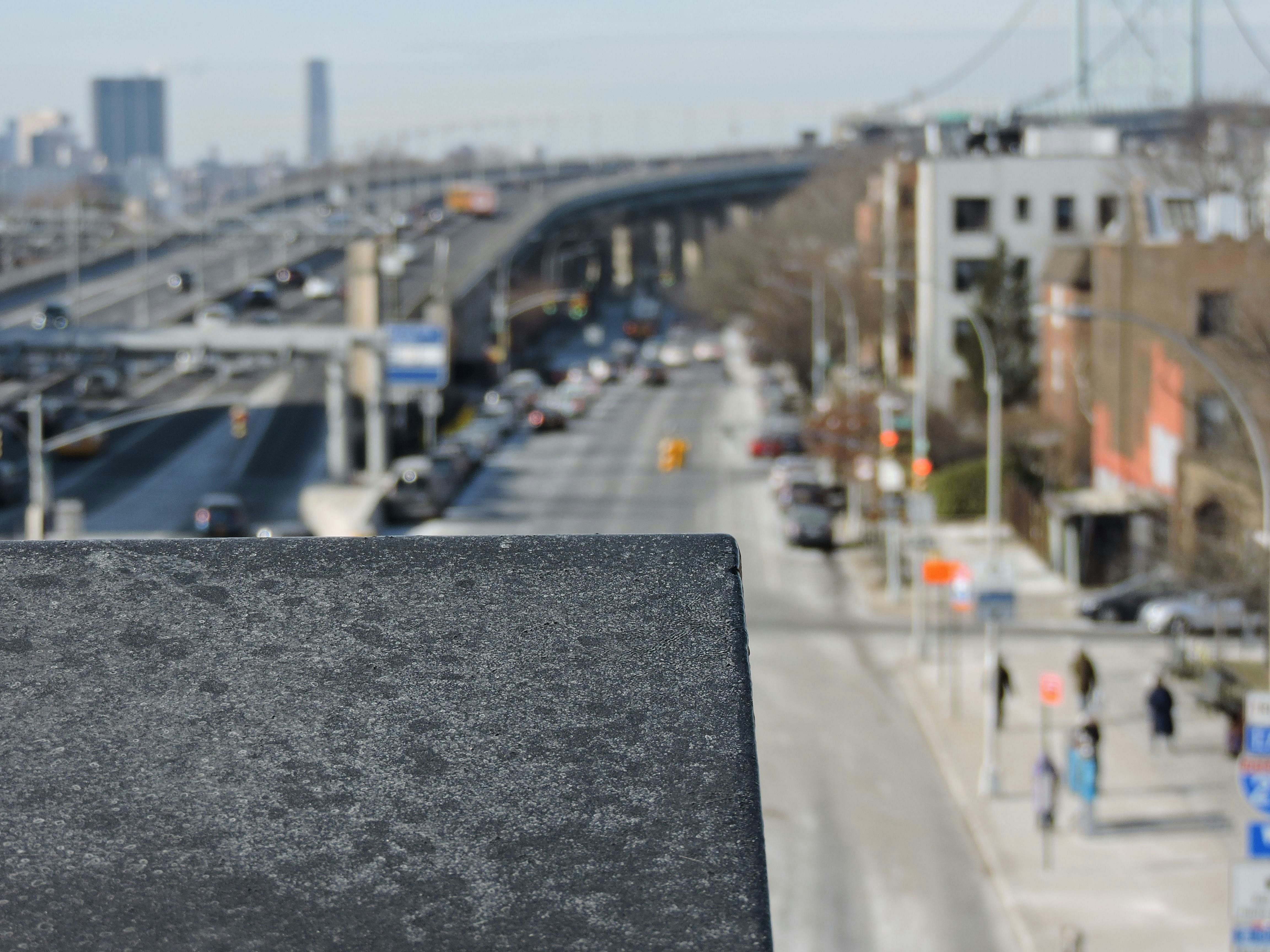 View of a busy highway and city street with blurred pedestrians in the foreground on a sunny day.