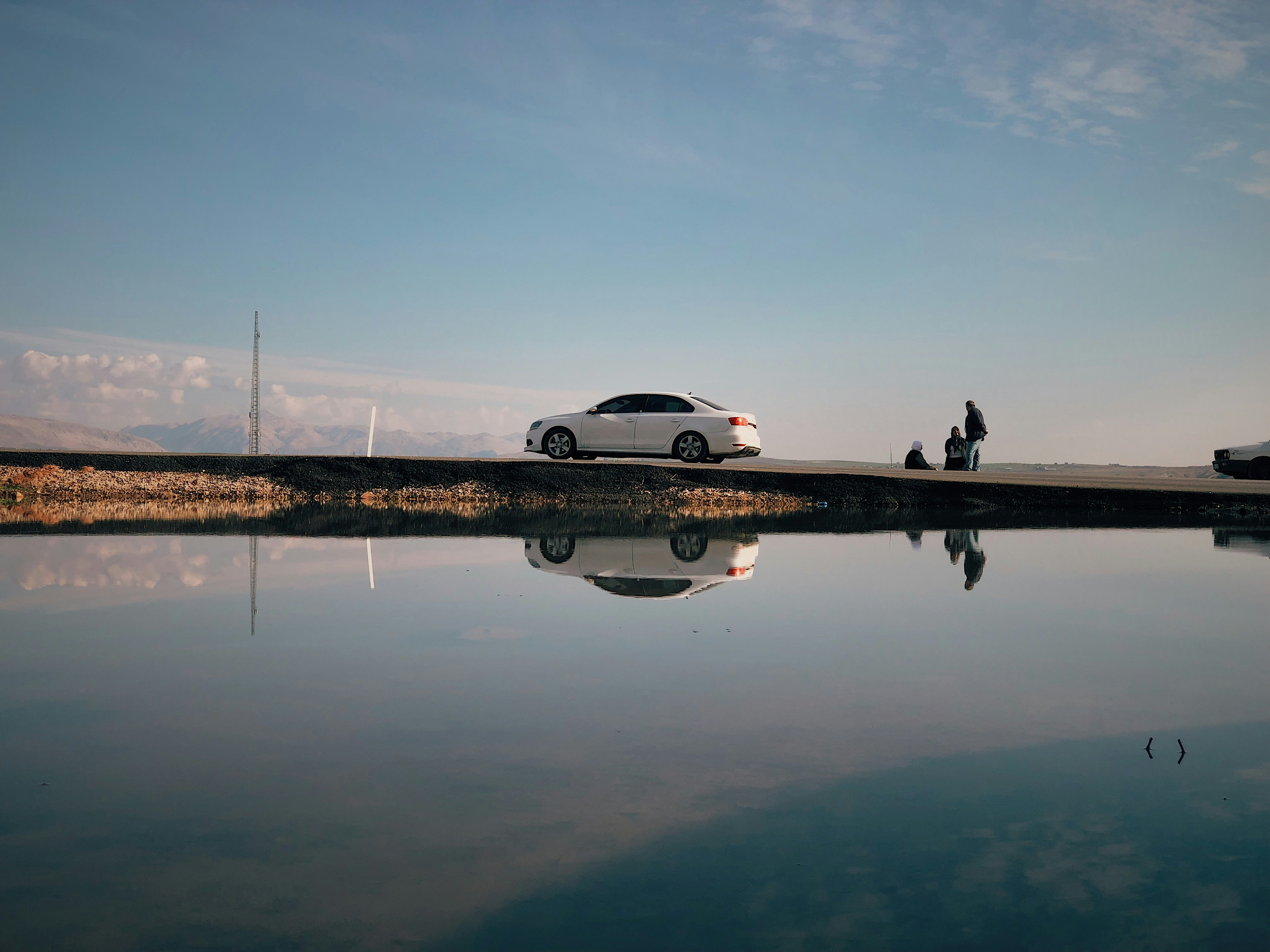 Edge of Silence: Silver Sedan on a Narrow Dike Over a Mirror-Water Horizon
