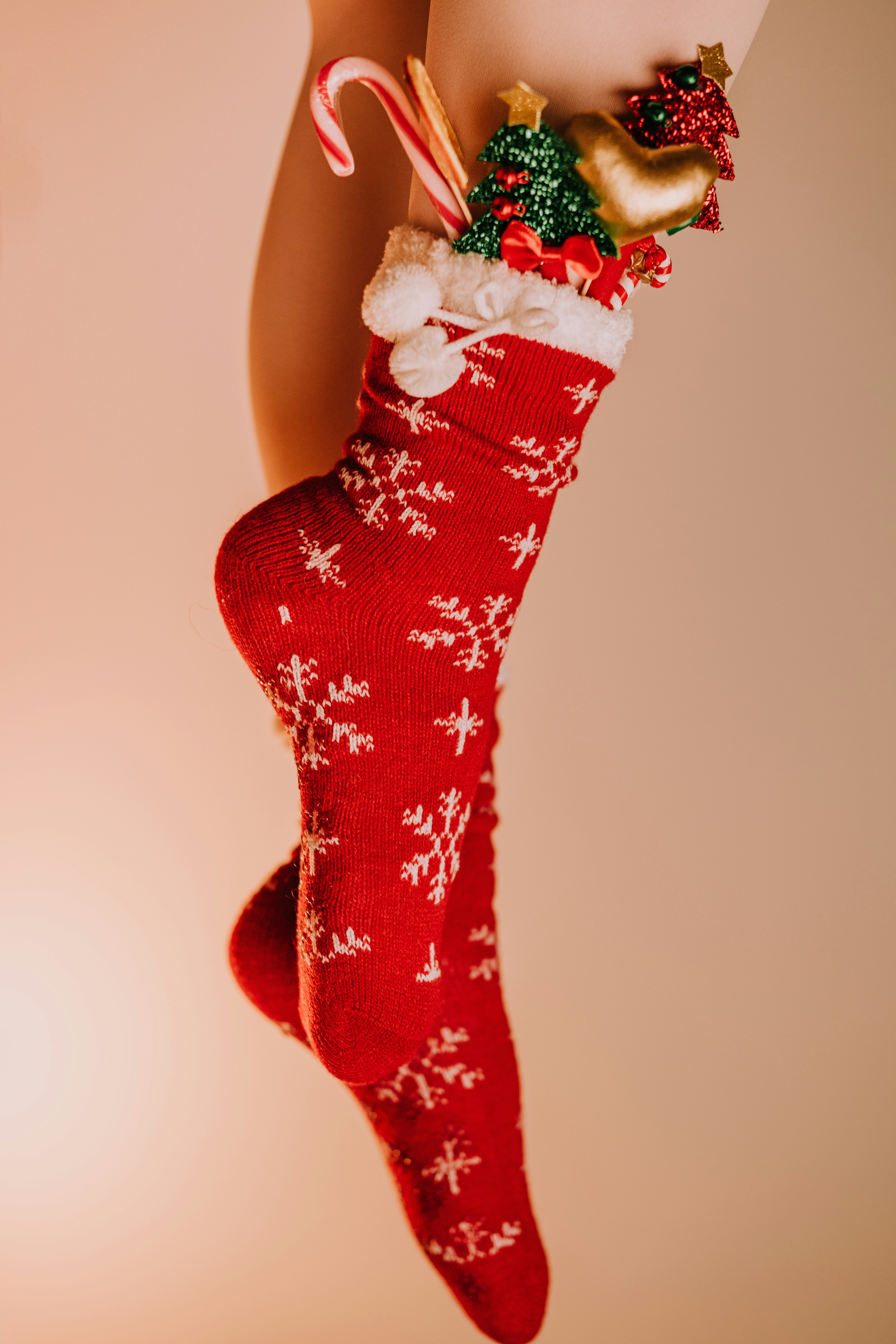 Red holiday sock adorned with festive decorations, including candy canes and ornaments, suspended against a warm backdrop.