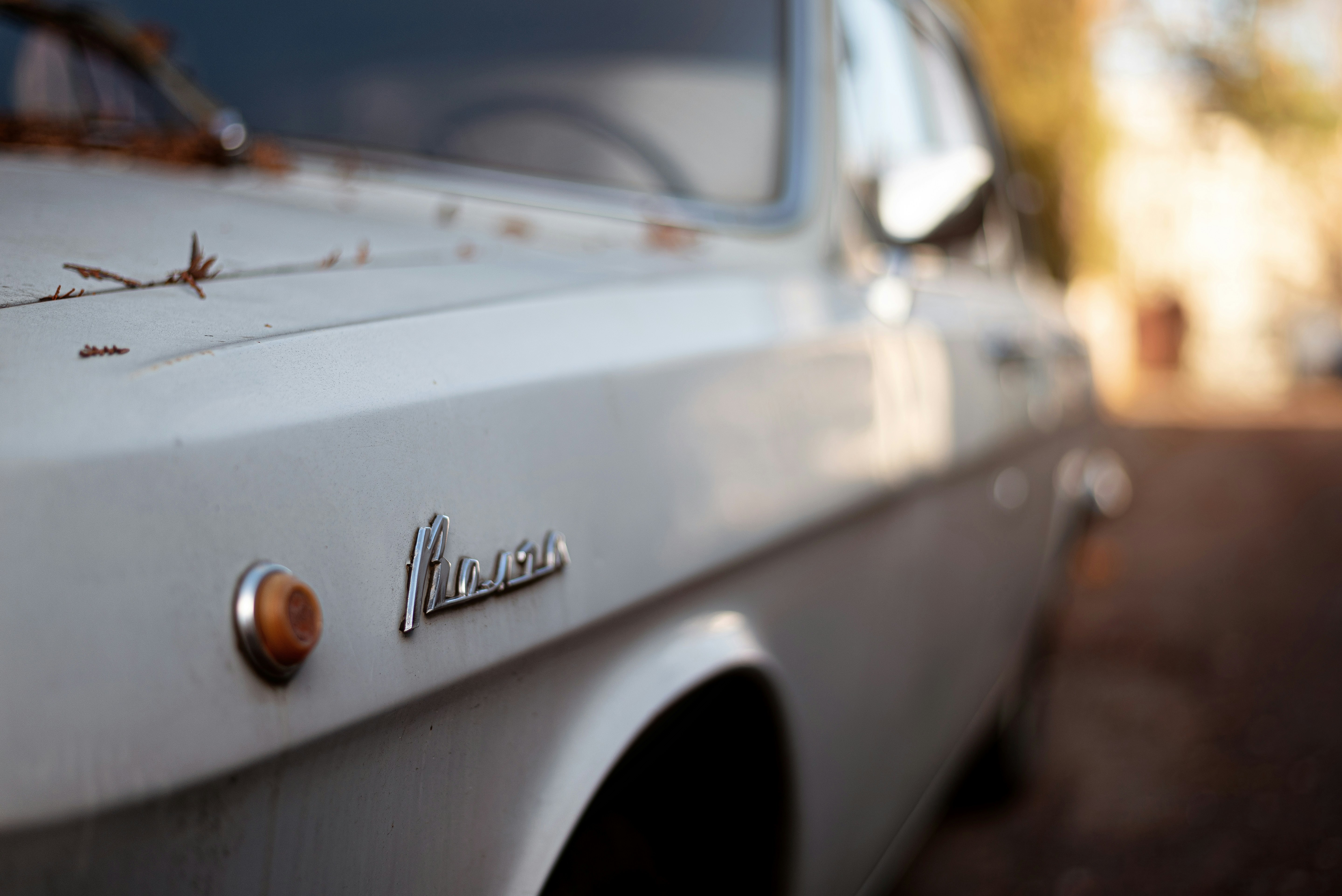 Emblem in Soft Focus: A Weathered Vintage Blue Sedan Under Quiet Street Light