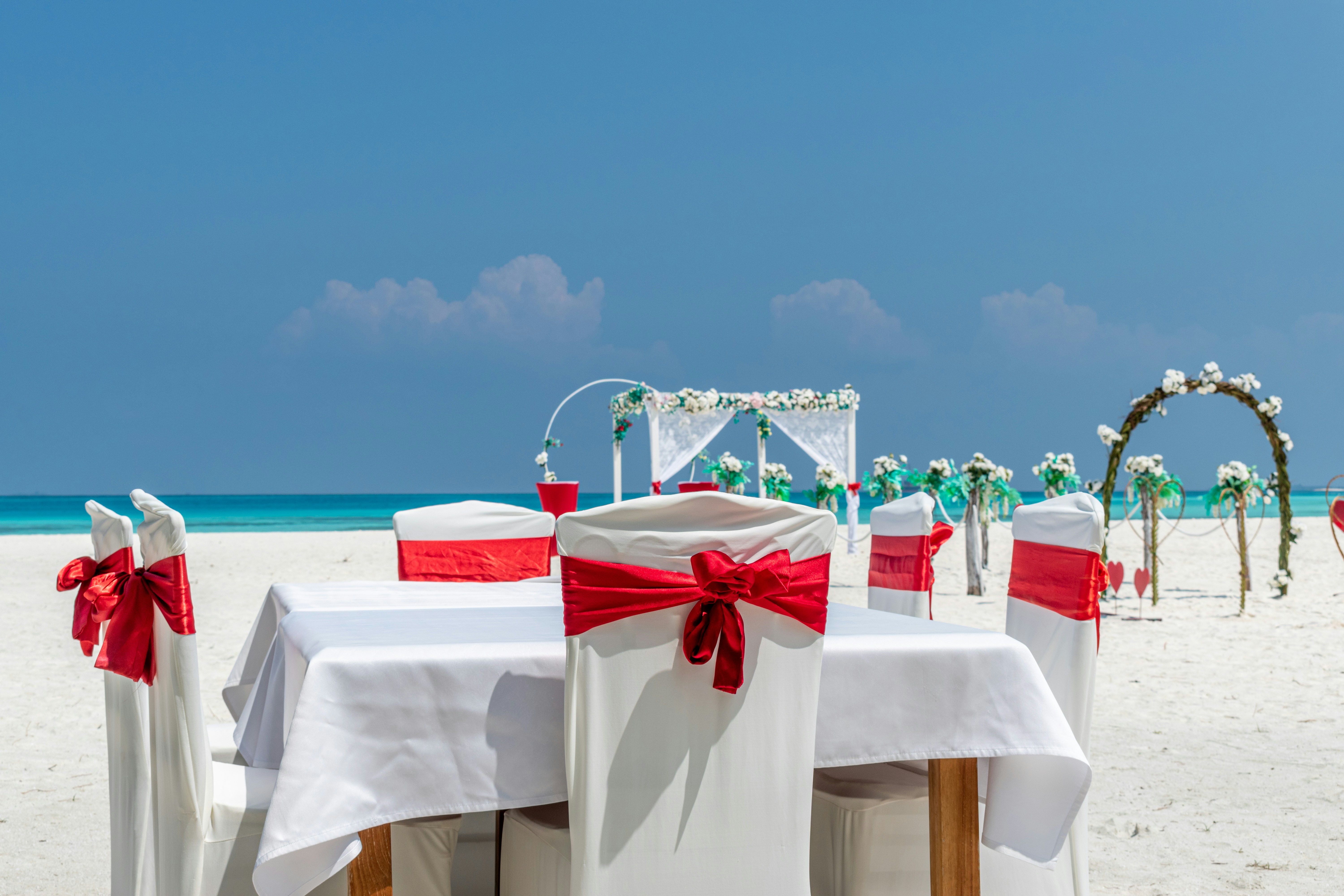 Crimson Accents on a Beachside Wedding: Chairs Framing a Seaside Arch
