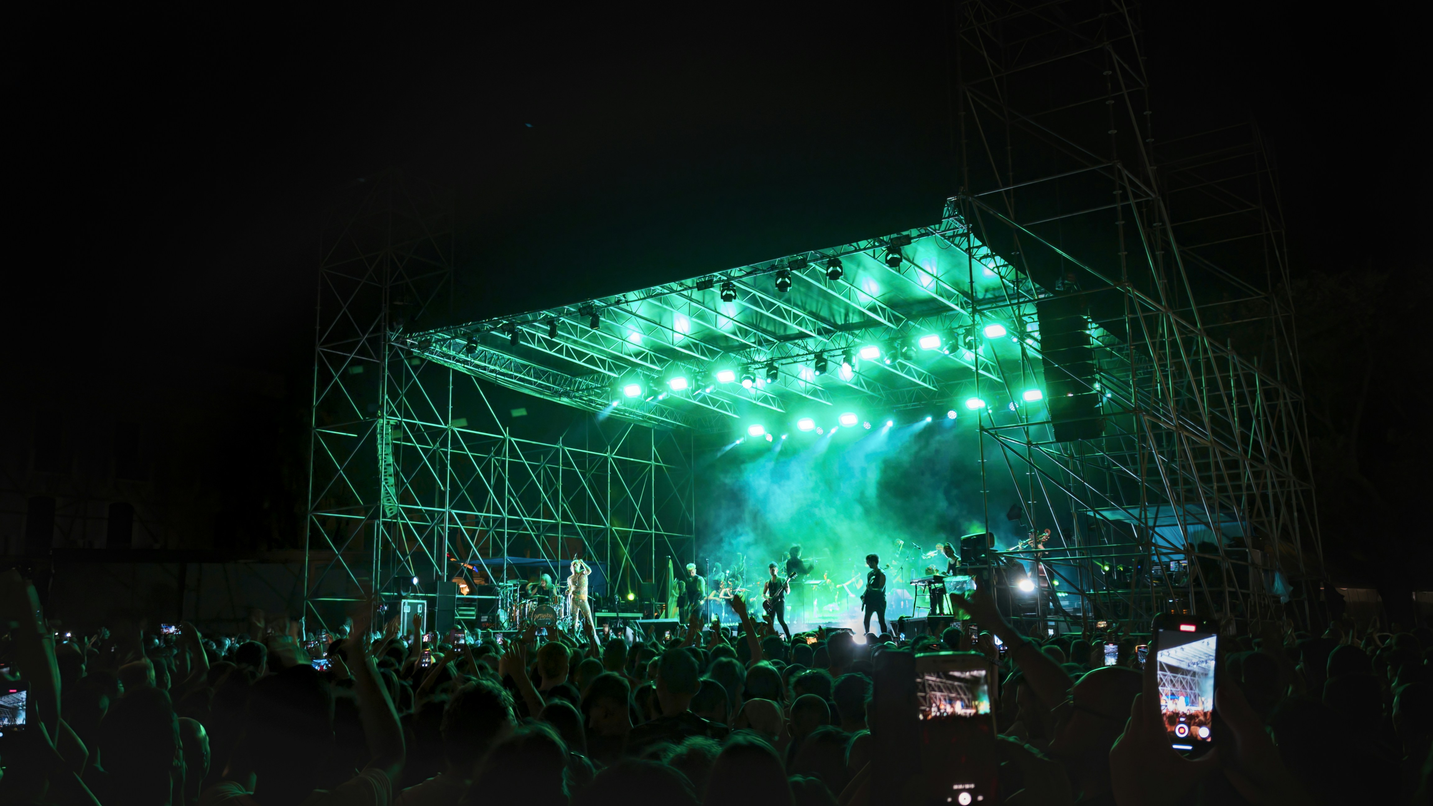 Concert scene featuring a lively band performing under vibrant green stage lights, surrounded by an enthusiastic crowd holding up their phones.